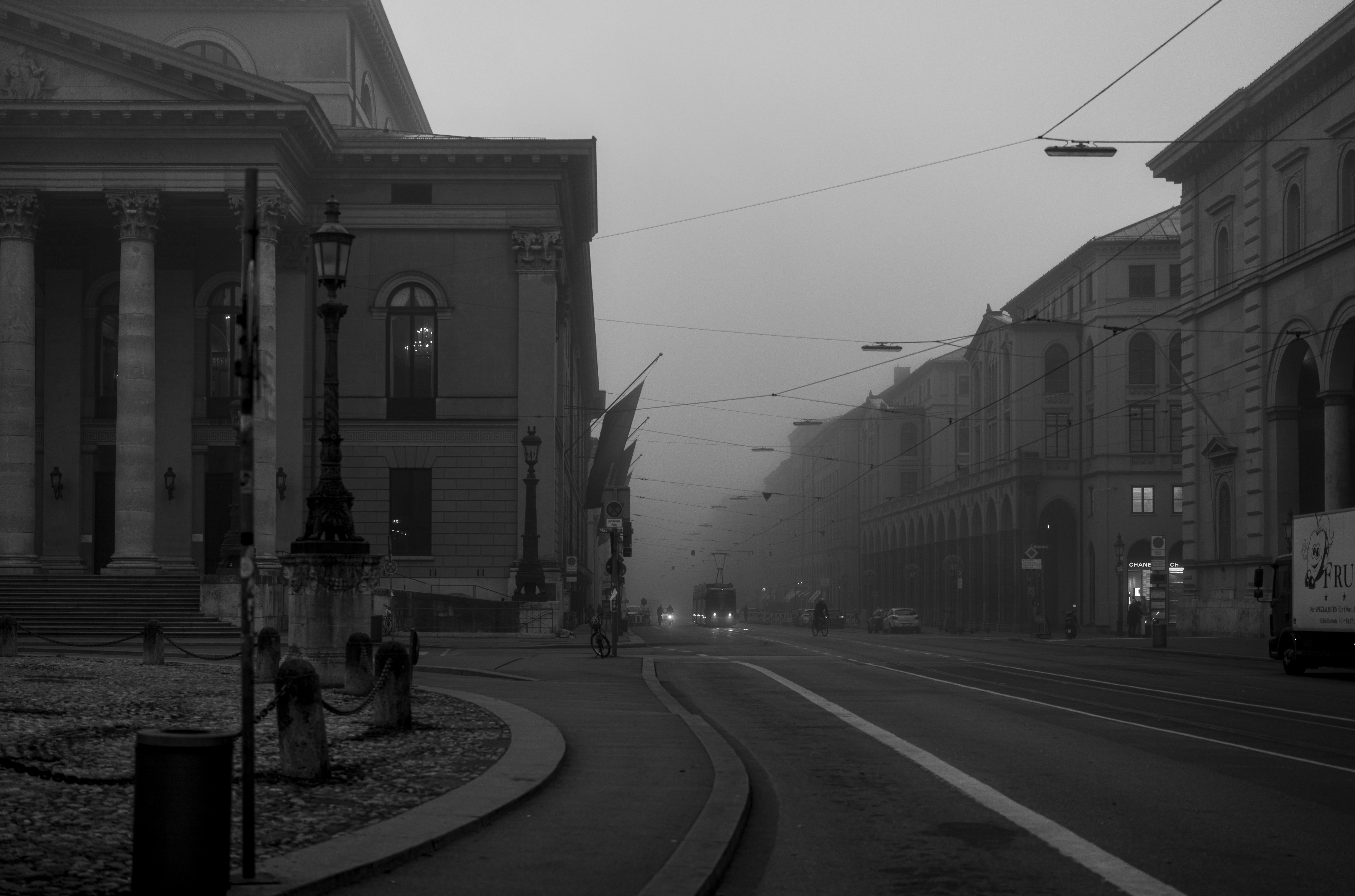 Historic architecture framed by a misty street scene, evoking a sense of mystery and solitude. The monochrome palette enhances the atmospheric depth.