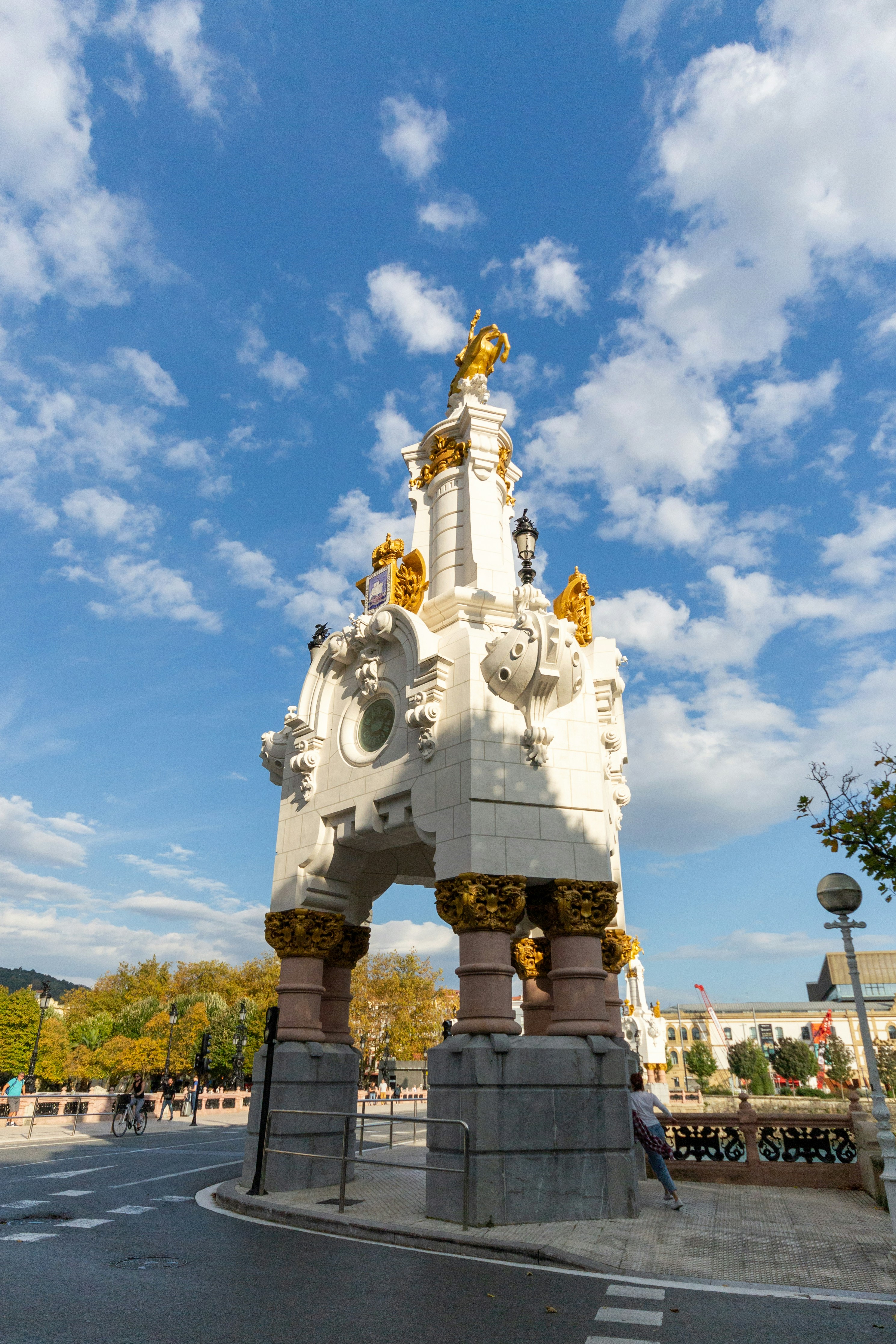 Elaborate architectural archway adorned with golden sculptures and intricate details against a vibrant sky. A blend of historical and modern elements in a public space.