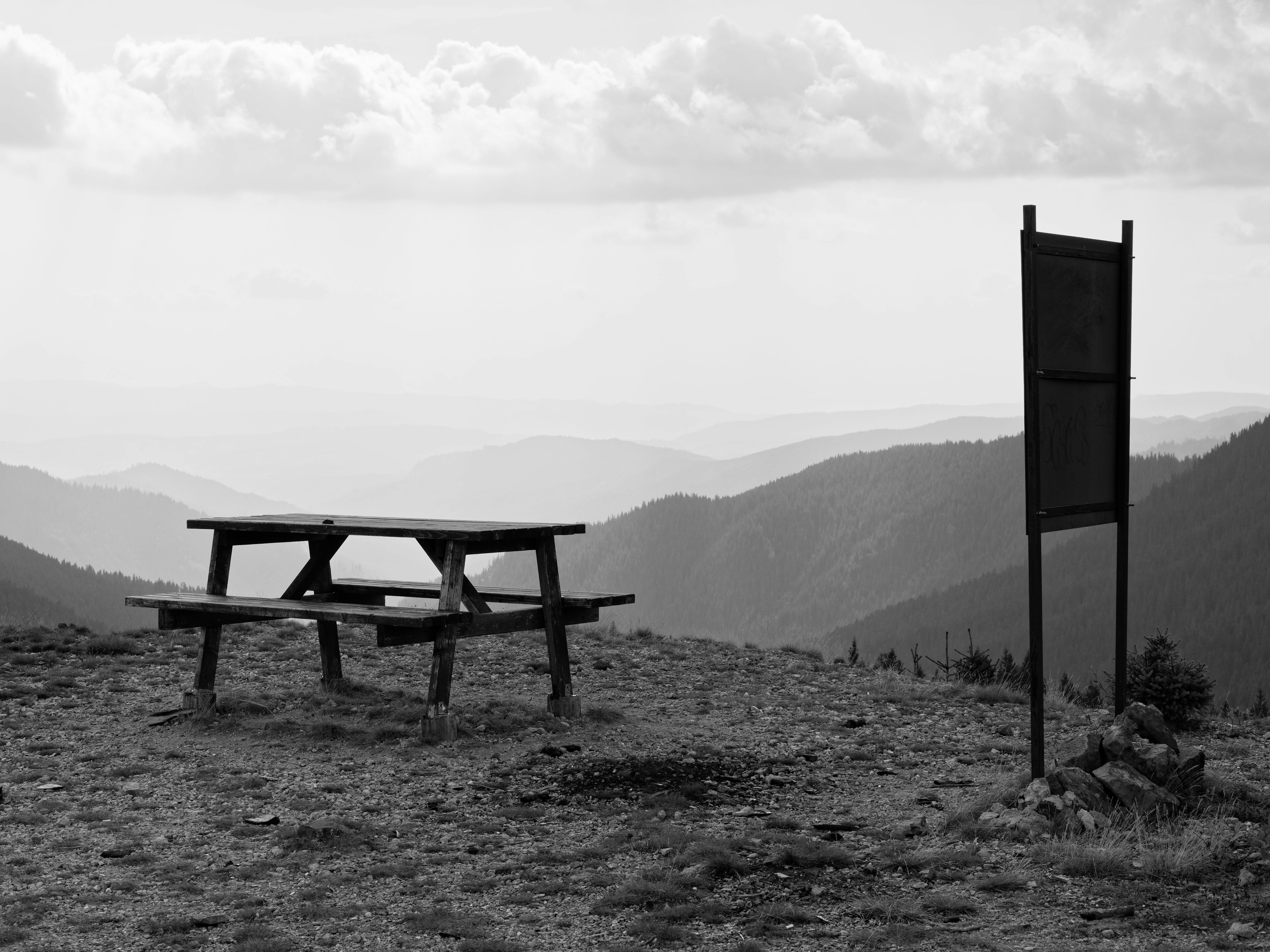 Wooden picnic table and signpost on a rocky hilltop overlooking misty mountain ranges.