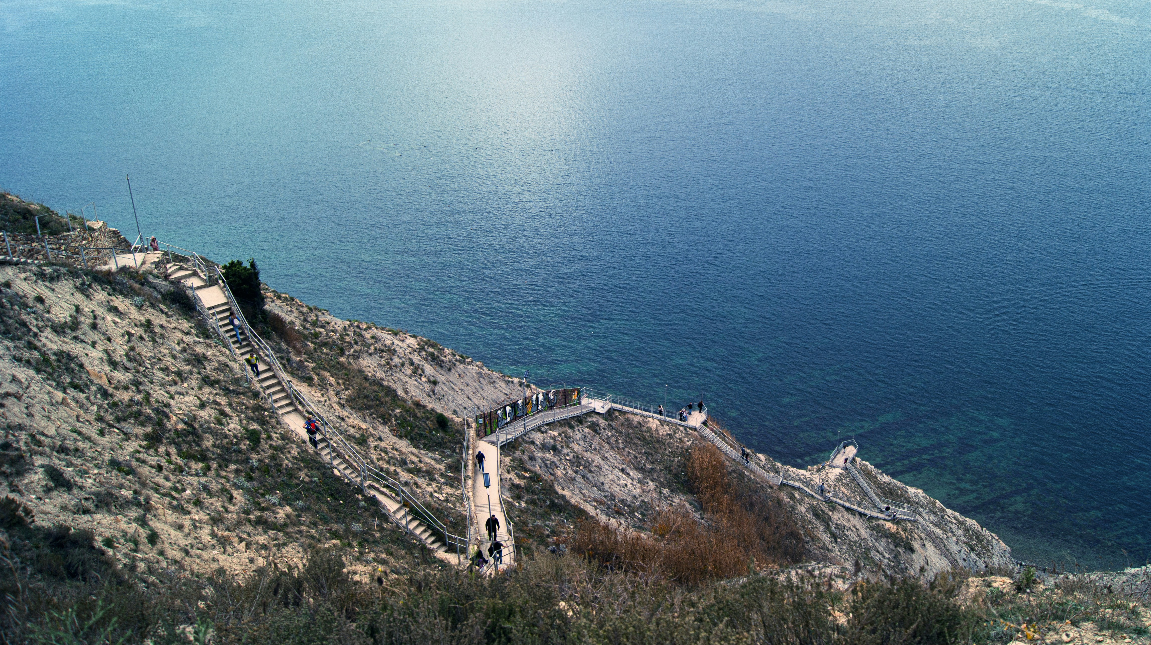 a group of people walking up a steep hill next to a body of water