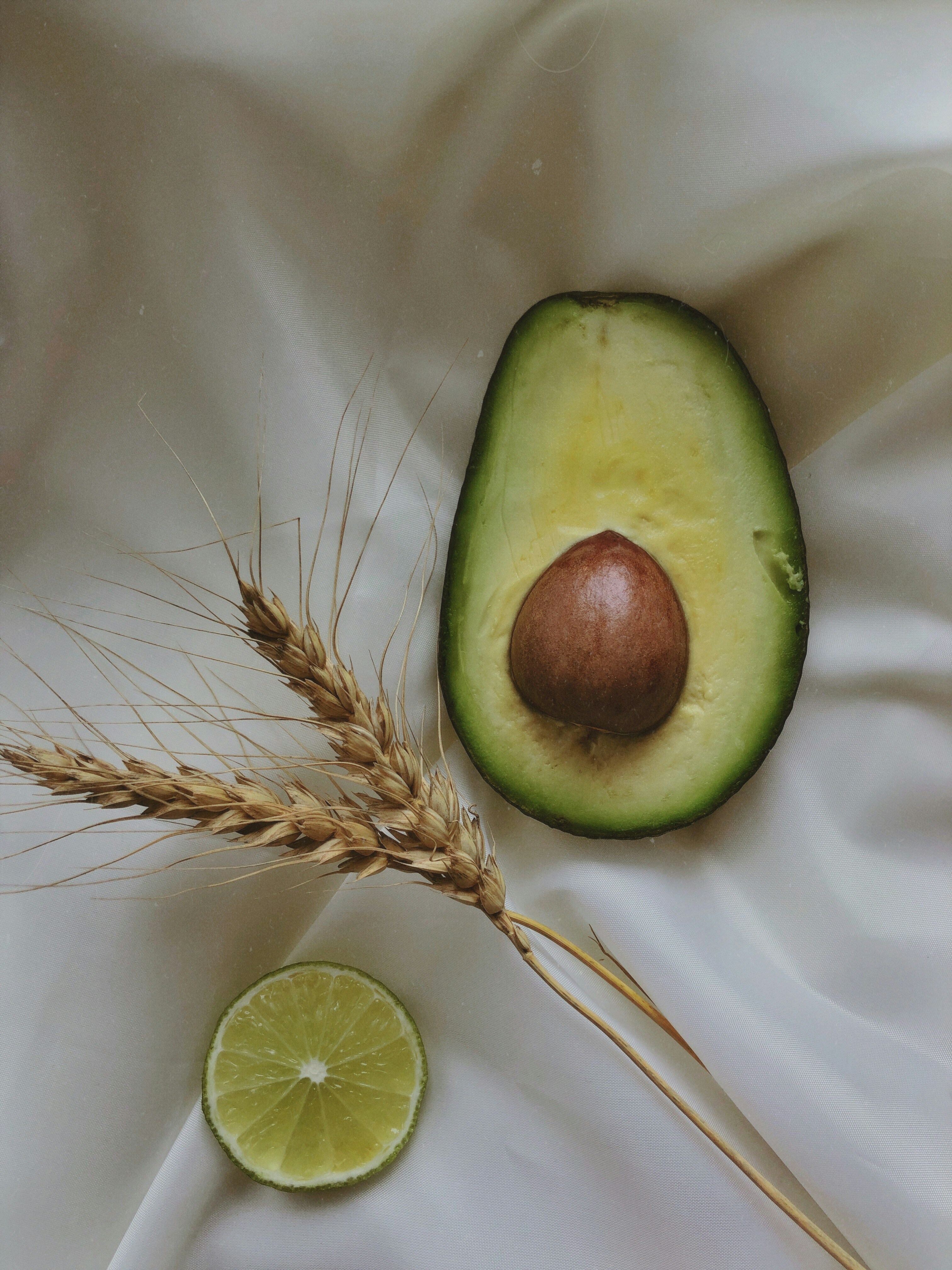 Avocado Half on White Satin: A Quiet Still-Life with Lime and Wheat