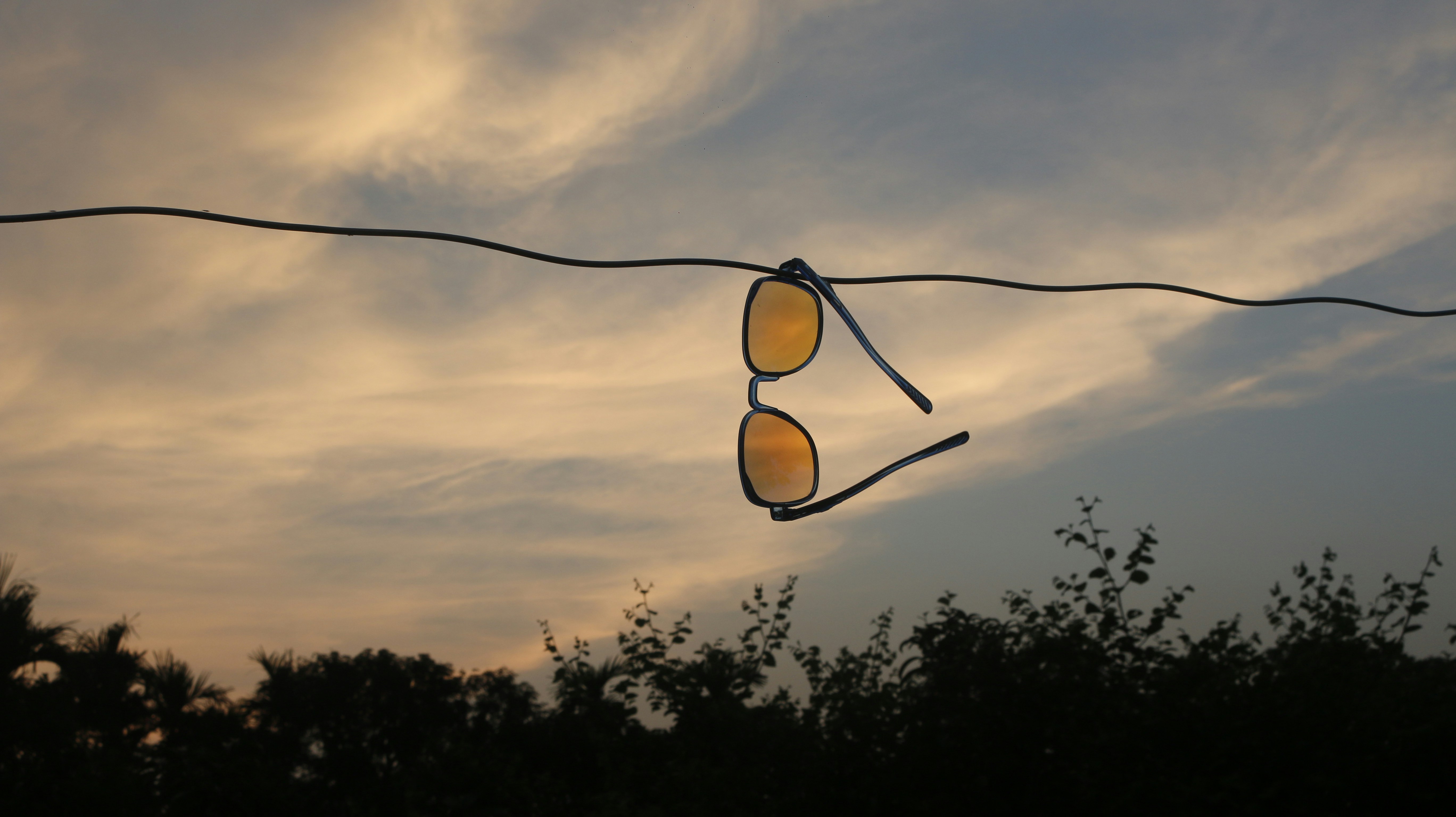 Dusk and Glass: Sunglasses Draped Across a Wire Over a Quiet Horizon