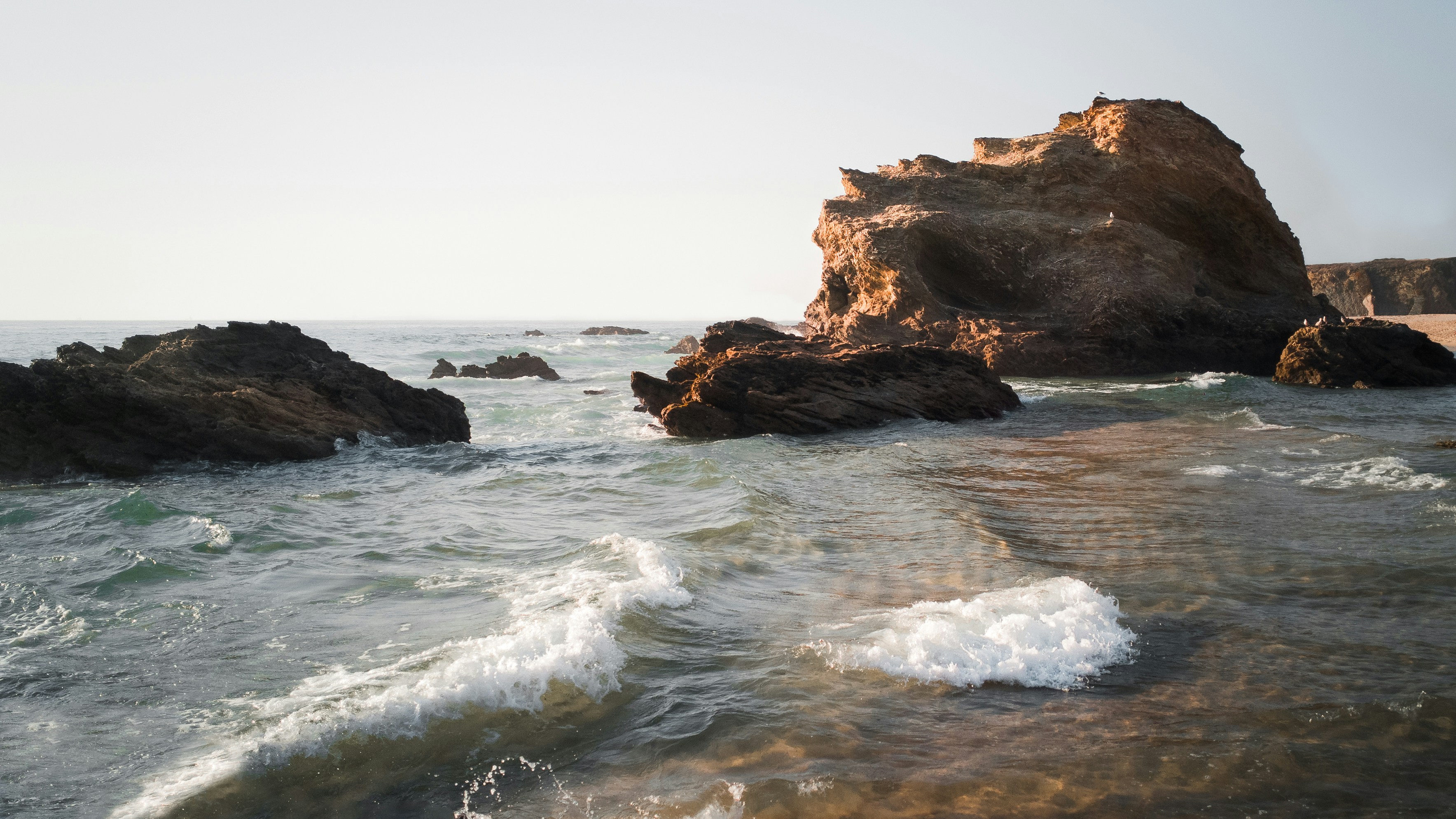 Foto zum Thema Ein felsiger Strand mit Wellen, die ins und aus dem ...