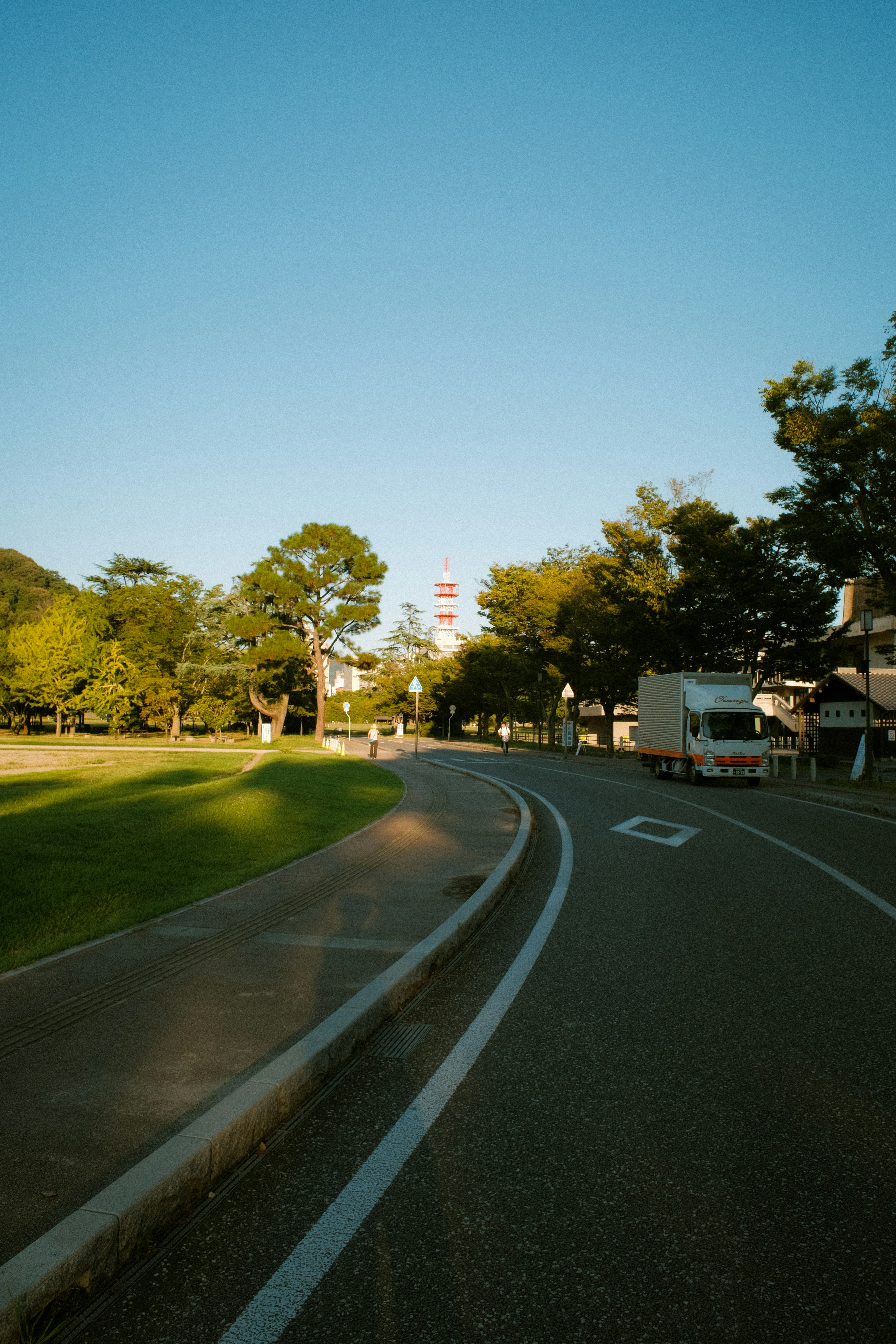 a truck driving down a curvy road next to a lush green park