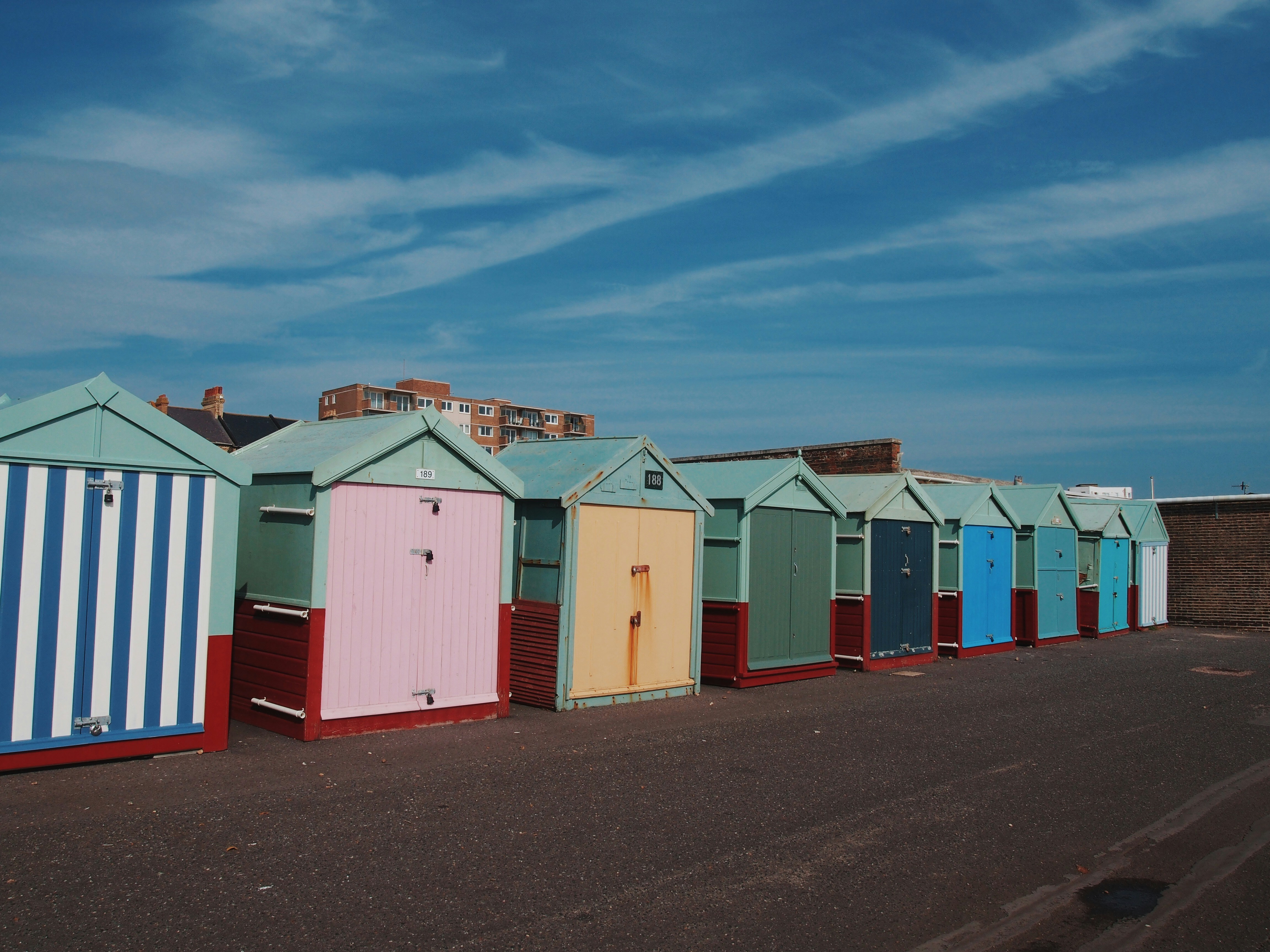 Row of vibrant beach huts lined against a clear blue sky, showcasing a variety of pastel colors and architectural styles.