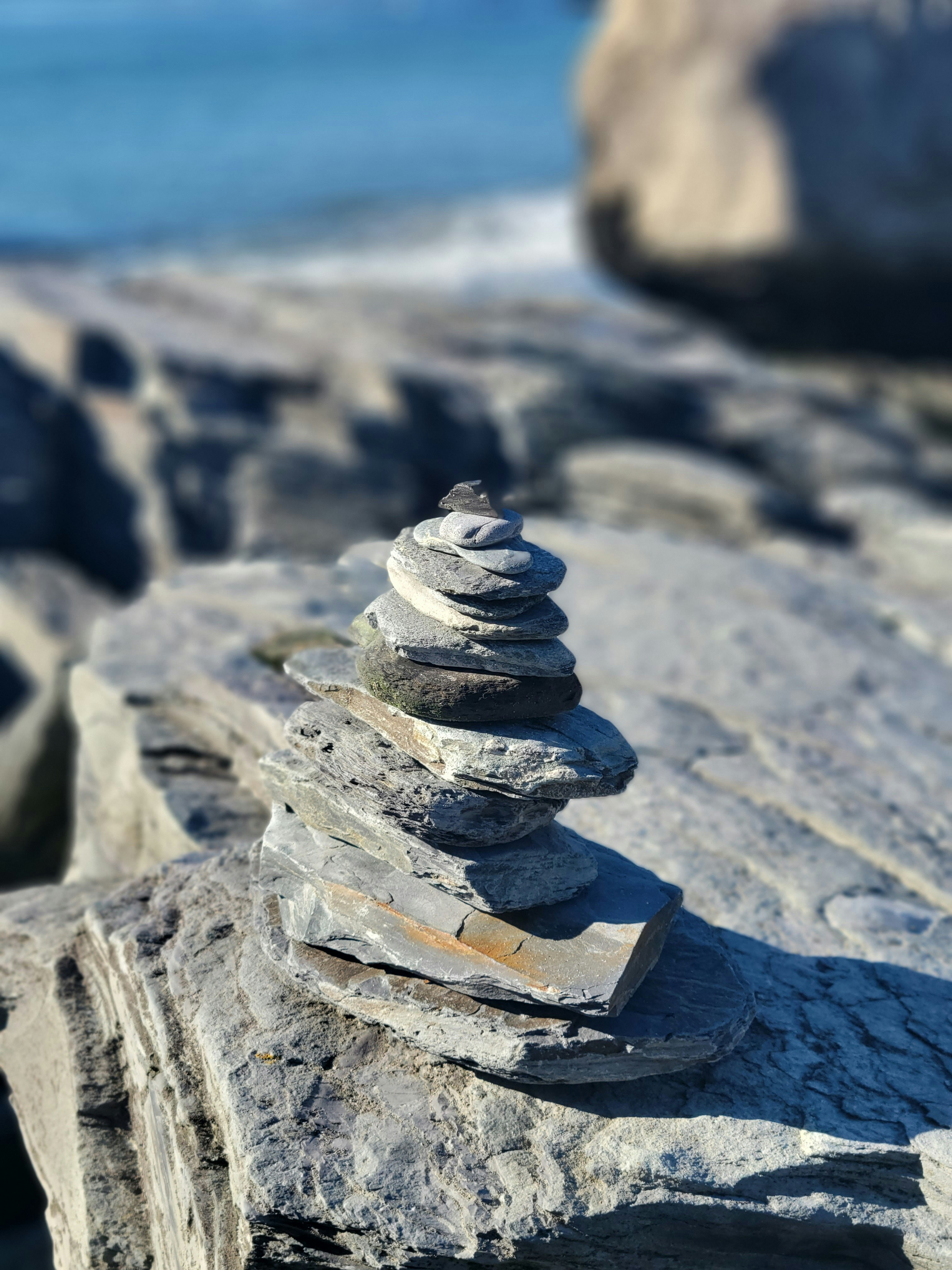 A meticulously balanced stack of stones atop a rugged rock formation, with a serene ocean backdrop. The arrangement showcases both nature's artistry and human craftsmanship.