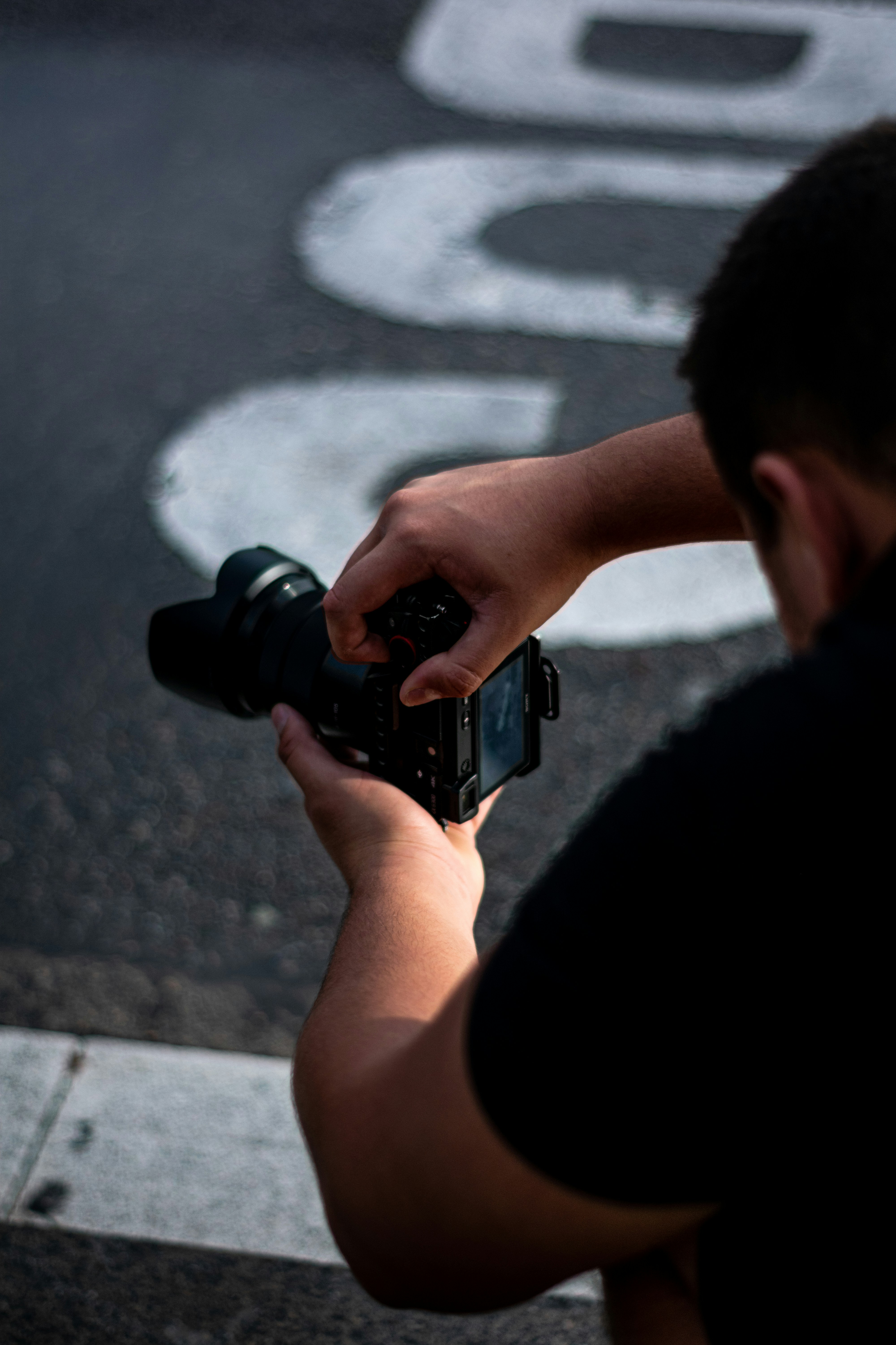 Photographer adjusting settings on a Nikon D3400, capturing a street scene with a painted road marking in the background.
