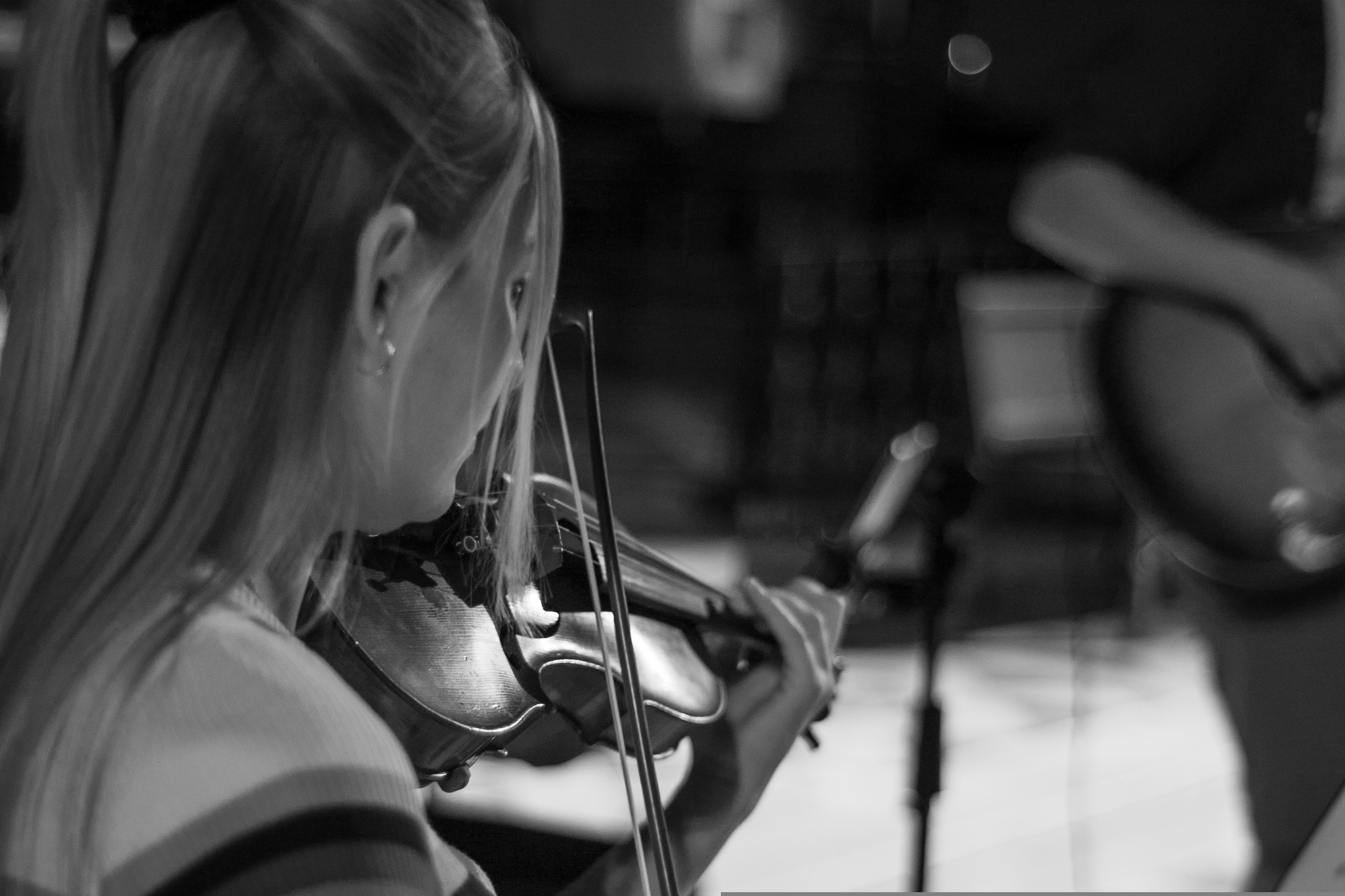 Young woman playing the violin in a dimly lit setting, immersed in her music. The focus is on her technique and the instrument's details.