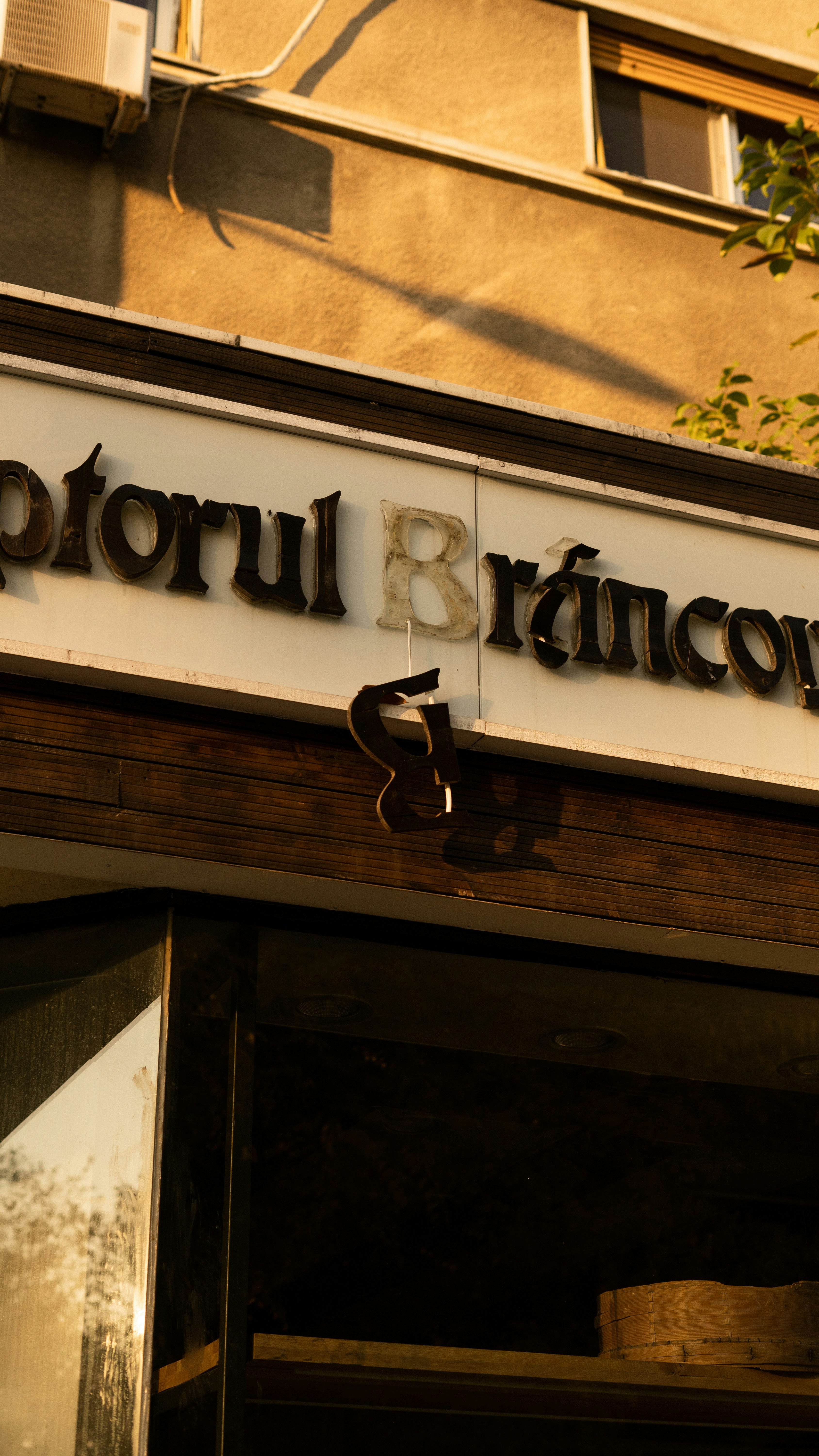 Amber Hour Signboard: Weathered Letters and a Hanging Ornament on a Romanian Shopfront