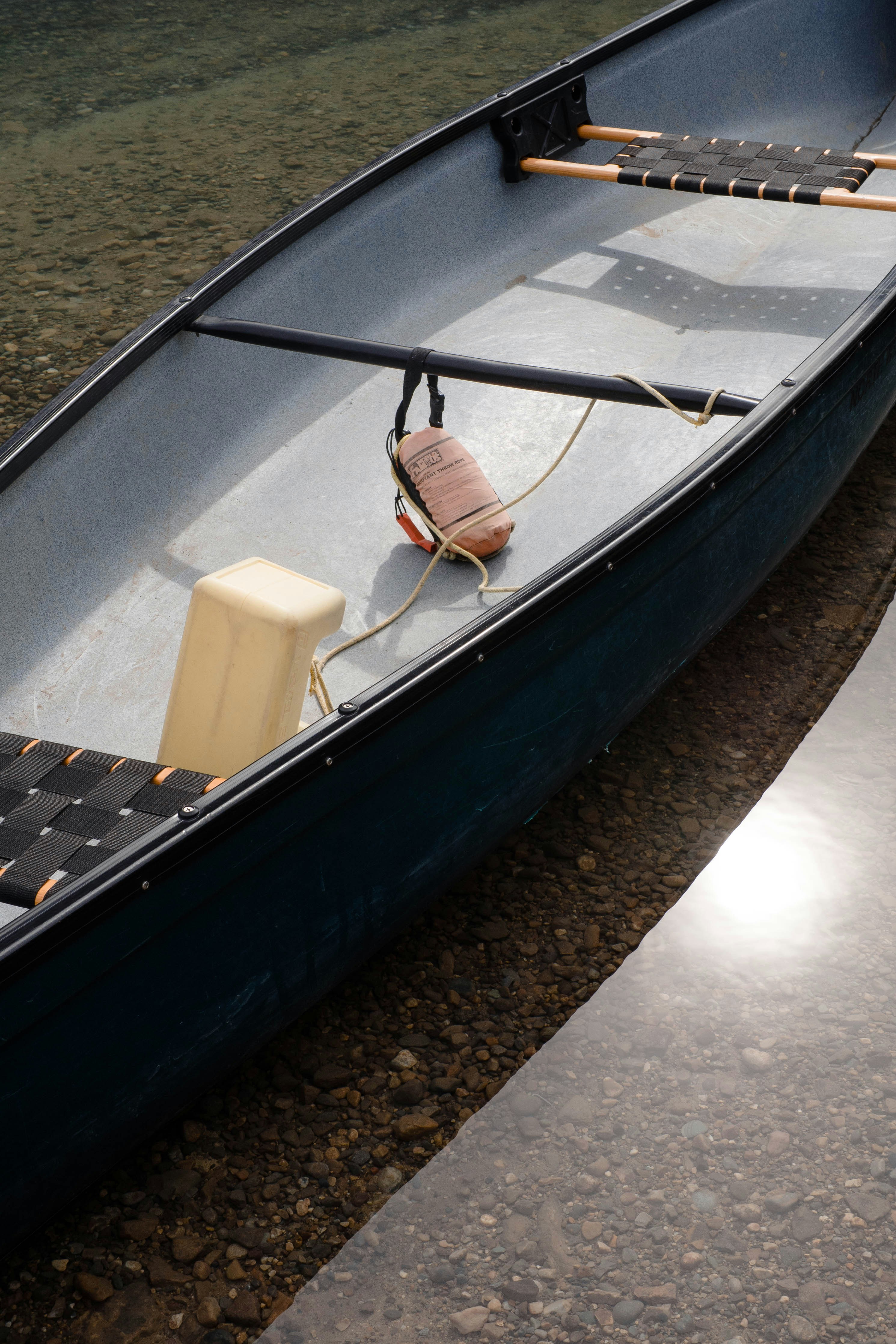 Sunlit Canoe Interior: A Tidy Scatter of Gear by the Pebble Shore