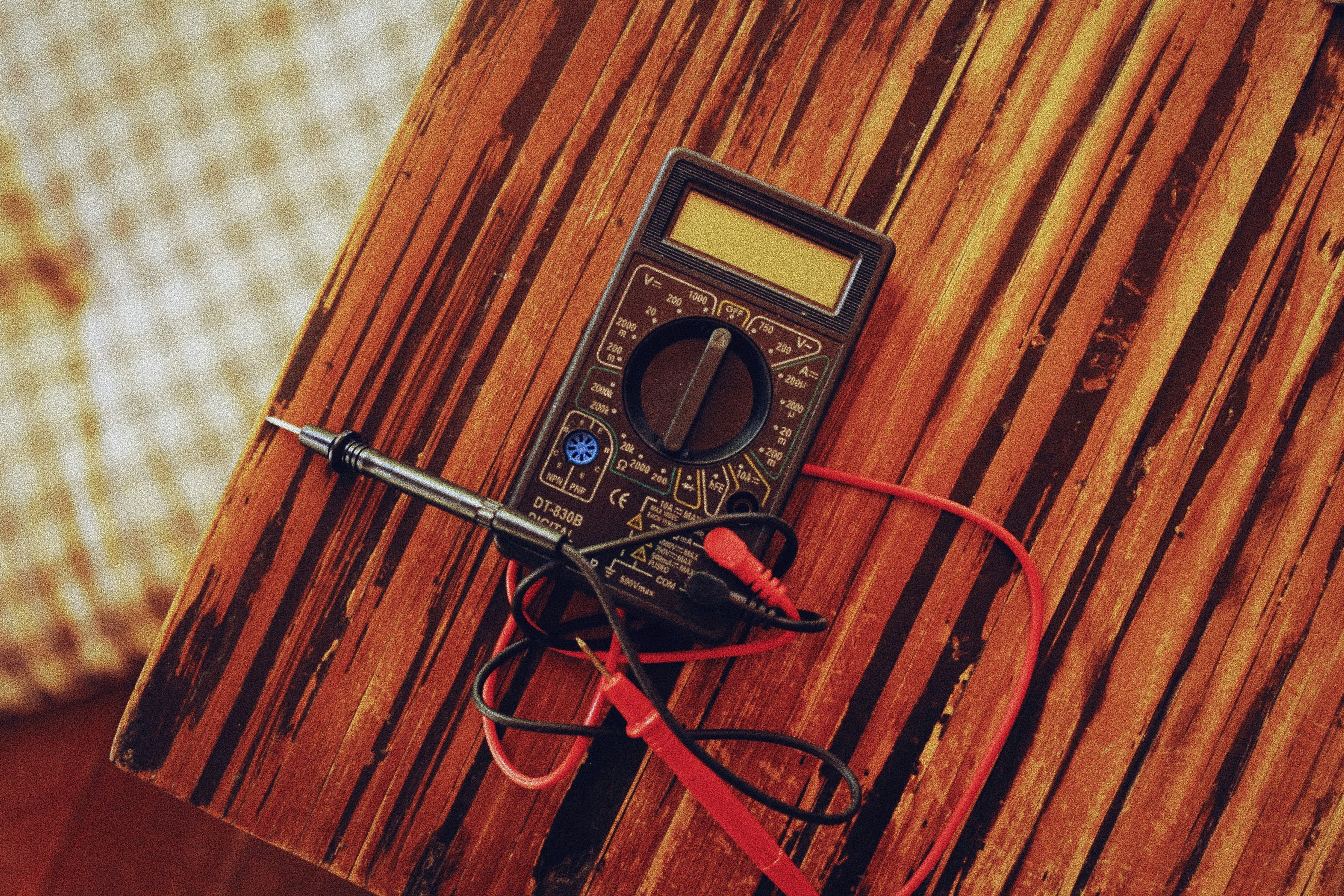 Digital multimeter resting on a wooden surface, showcasing its dials and leads for electrical measurements.