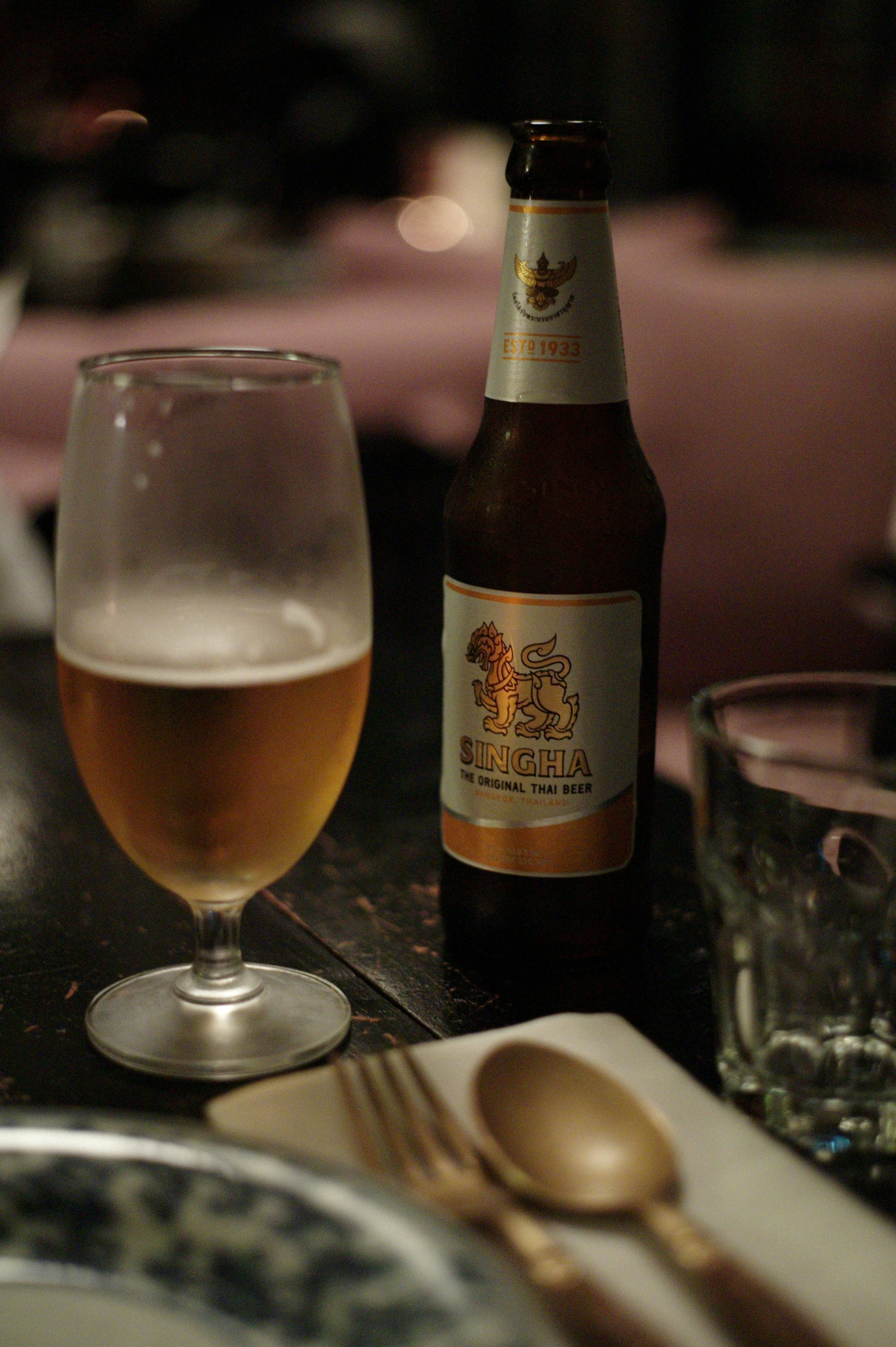 Singha beer bottle beside a half-filled glass on a dimly lit table, evoking a cozy dining atmosphere.