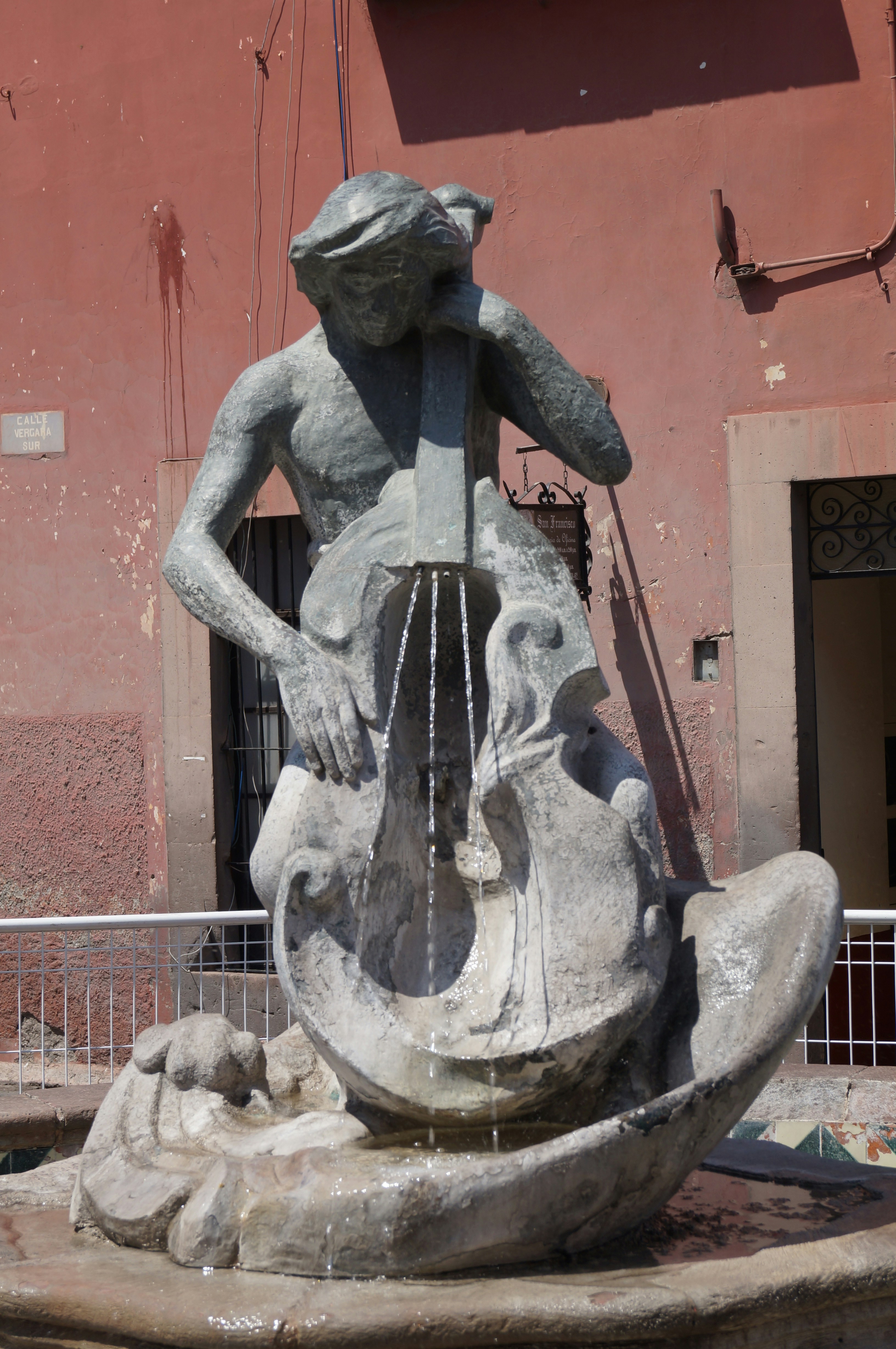 A sculptural fountain featuring a figure playing an instrument, with water cascading from it into a shell-shaped basin.