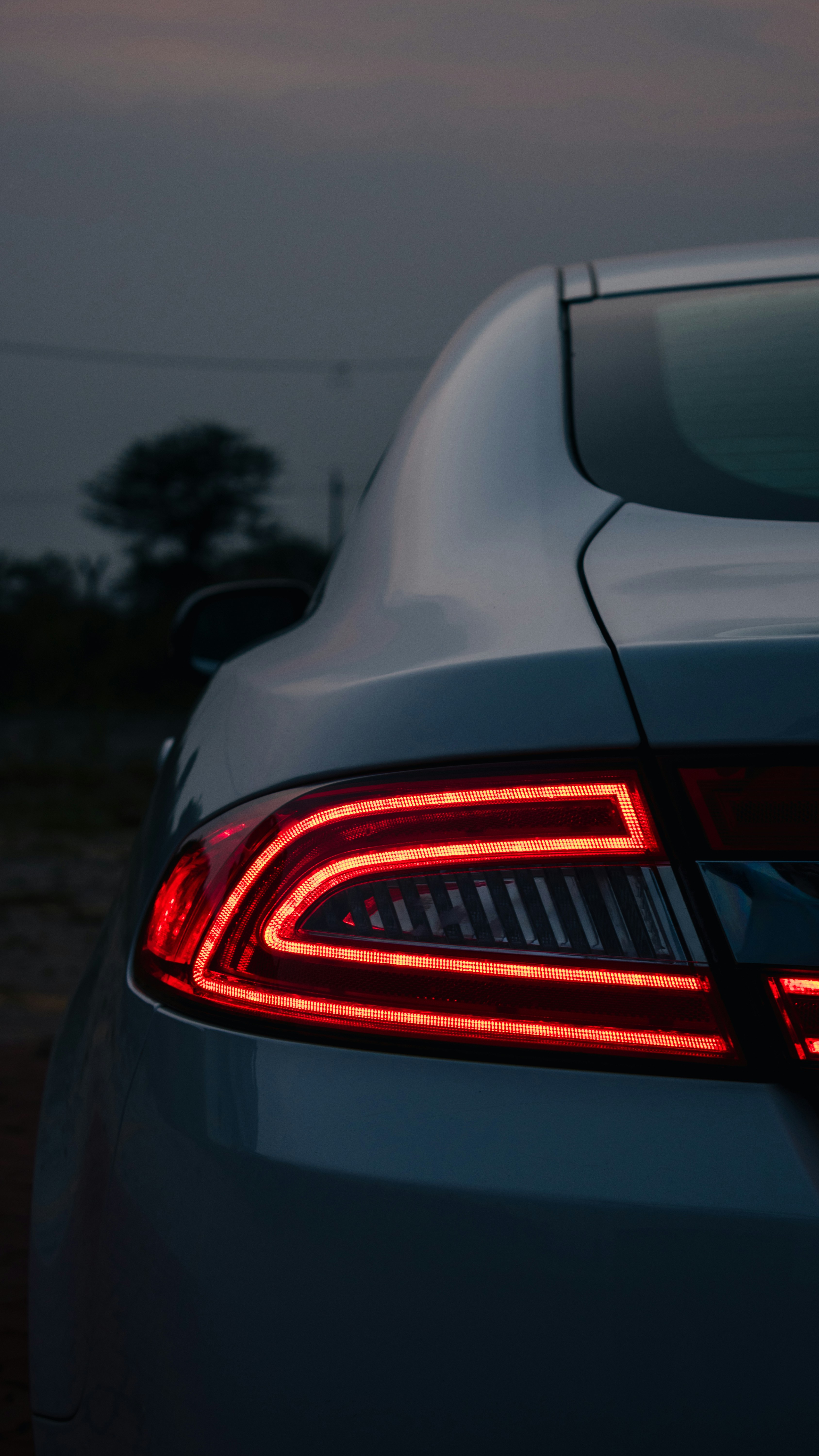 Close-up of a sleek car's illuminated tail light against a twilight sky, showcasing modern design and technology.