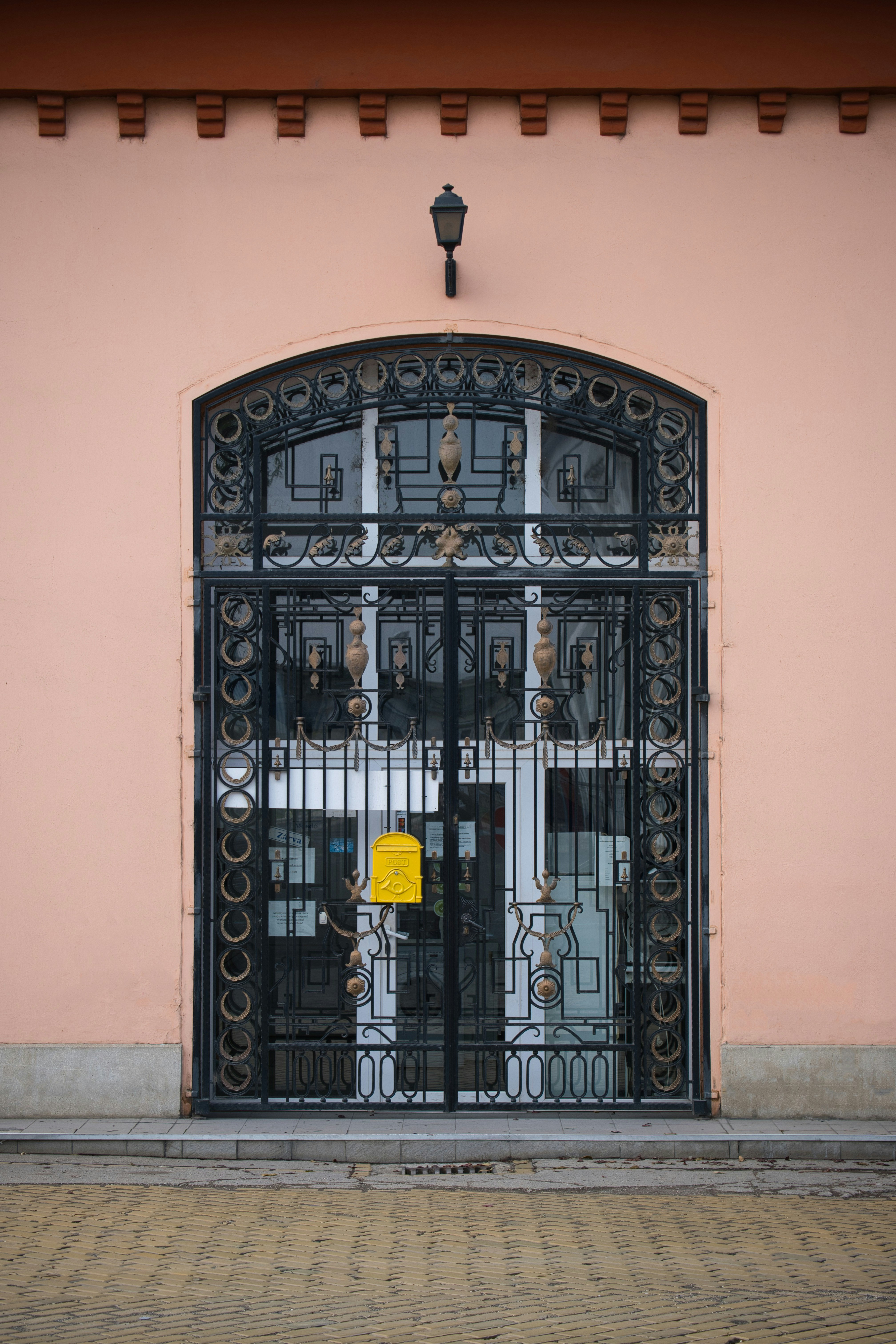 Intricate wrought iron gate framed by a pastel pink wall, featuring a bold yellow sign. The design reflects a blend of elegance and functionality.
