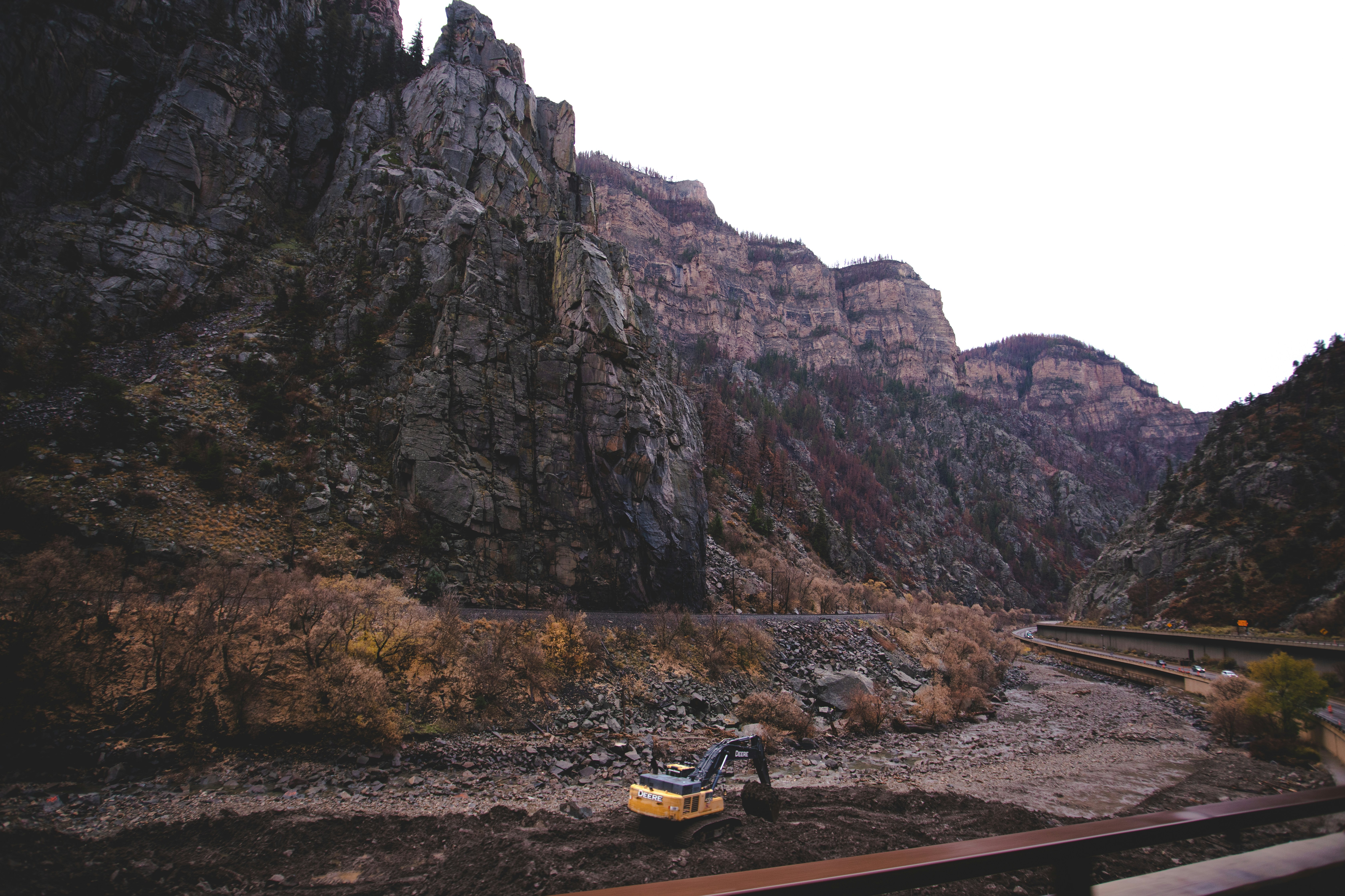 Heavy machinery working in a rocky riverbed surrounded by towering cliffs and rugged terrain. The landscape reflects a blend of nature and industrial activity.