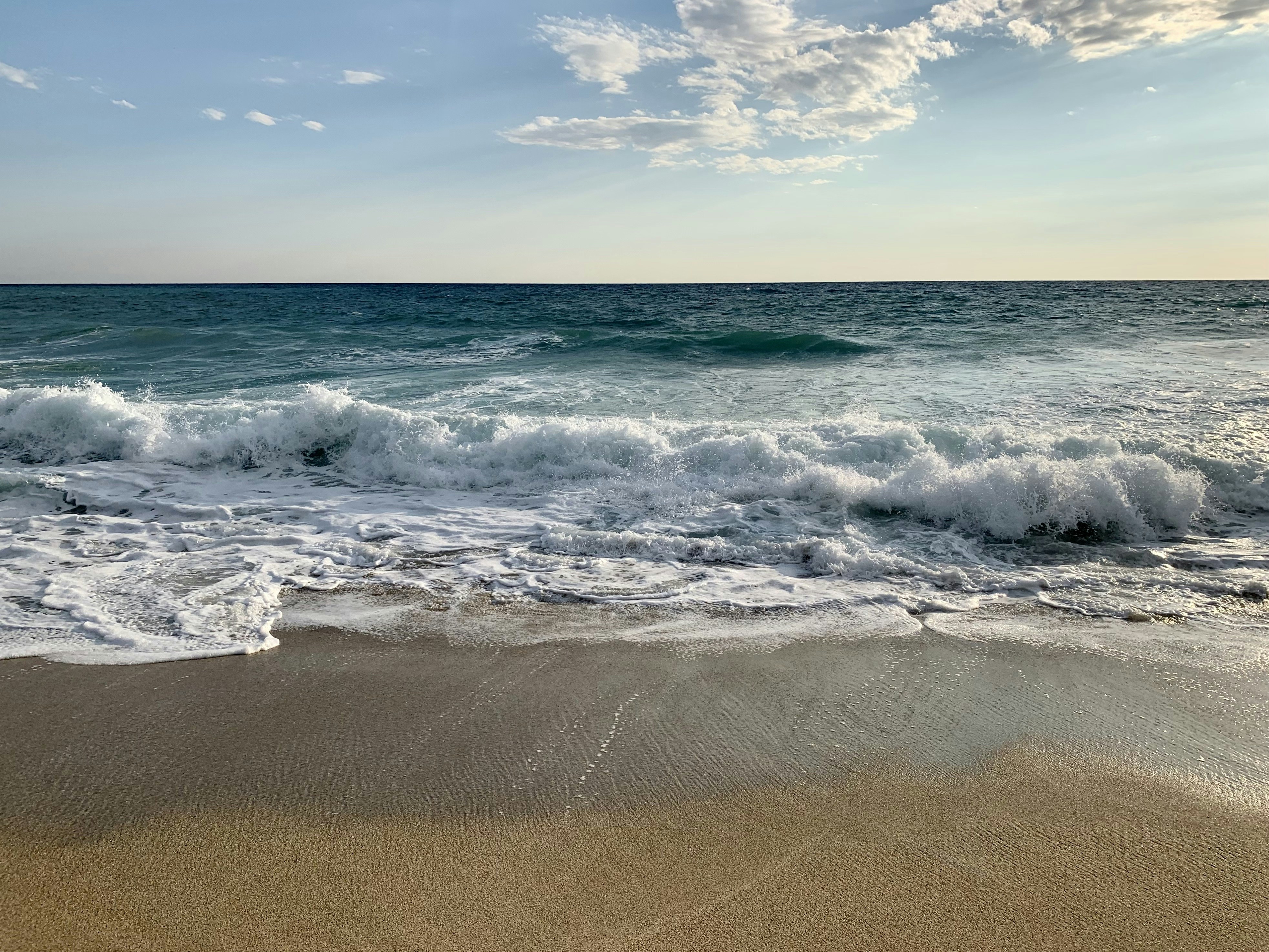 Gentle waves caress the sandy beach under a partly cloudy sky at Alanya, Turkey.