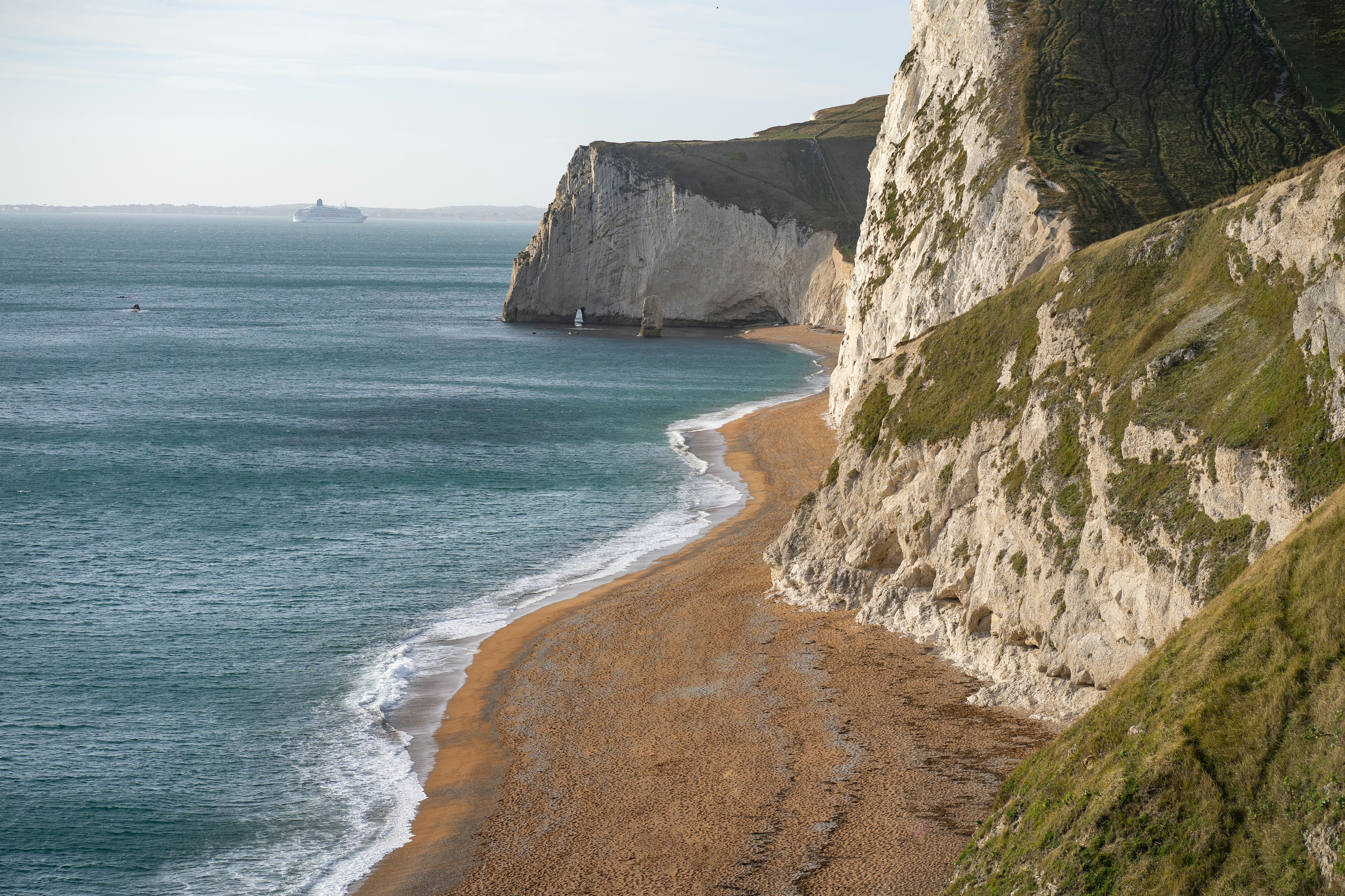 Cliffs towering over a sandy beach with a boat visible on the distant ocean.