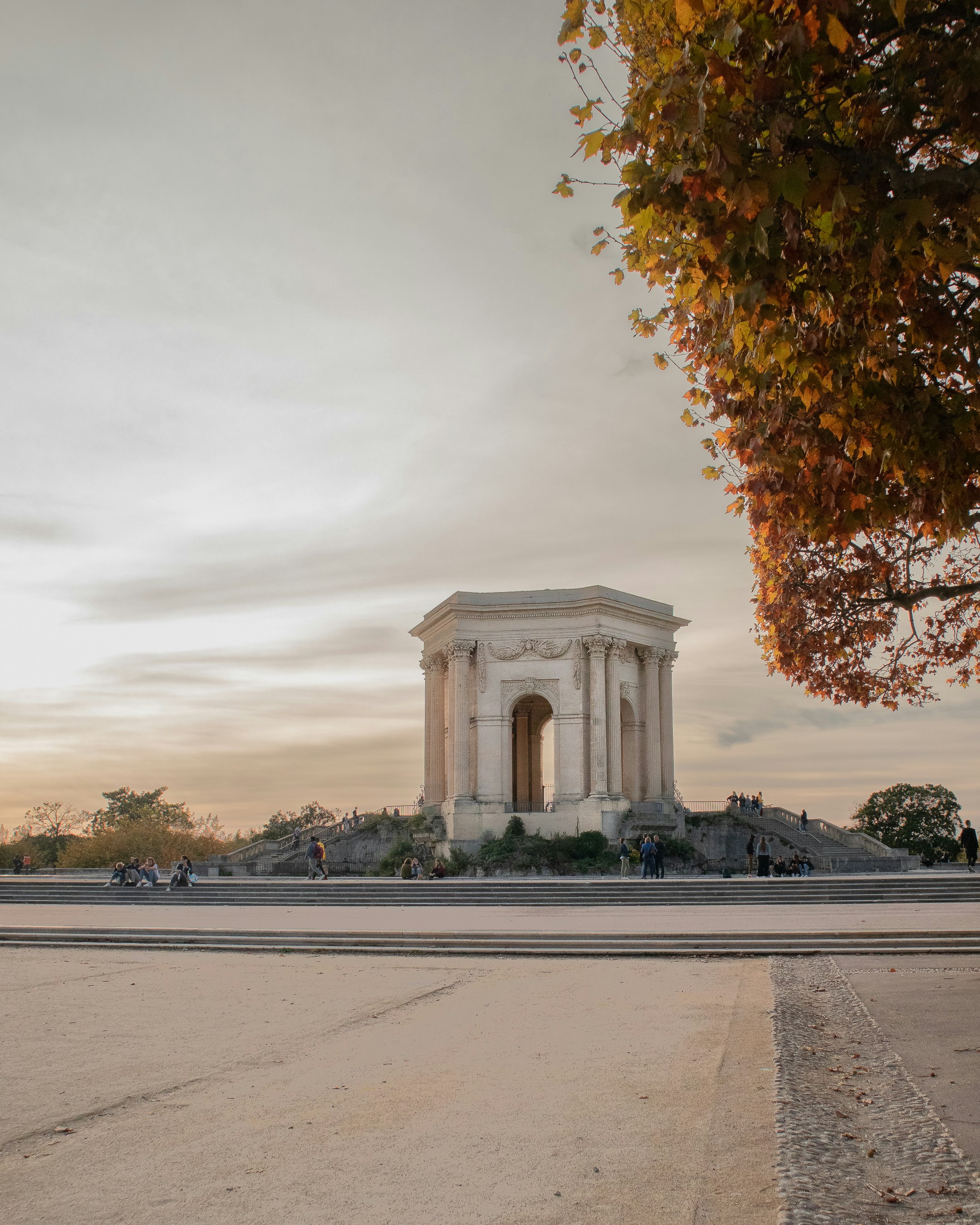 Historic monument framed by vibrant autumn foliage under a soft sunset sky. Visitors enjoy the serene atmosphere.