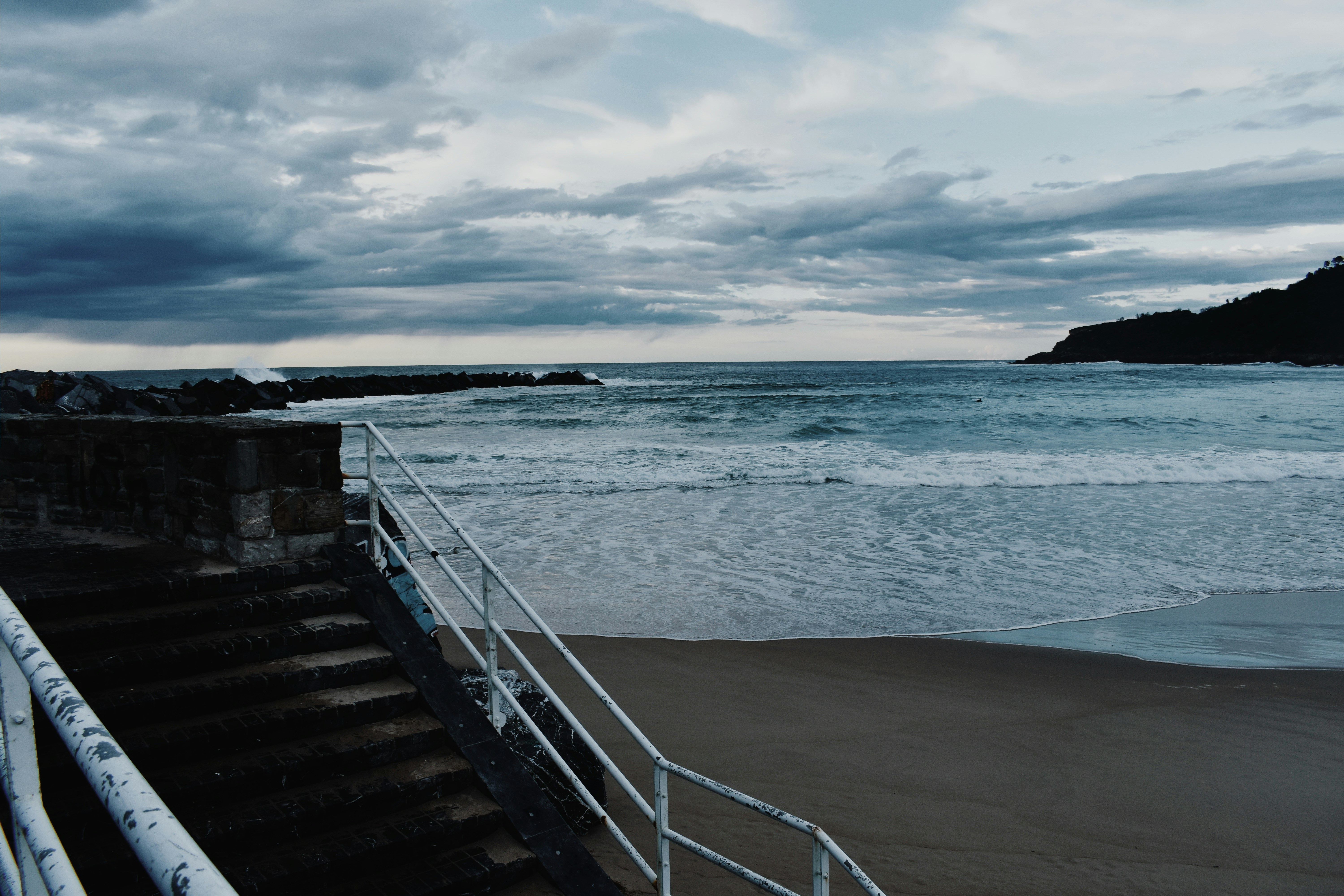 a stairway leading to the ocean with a cloudy sky