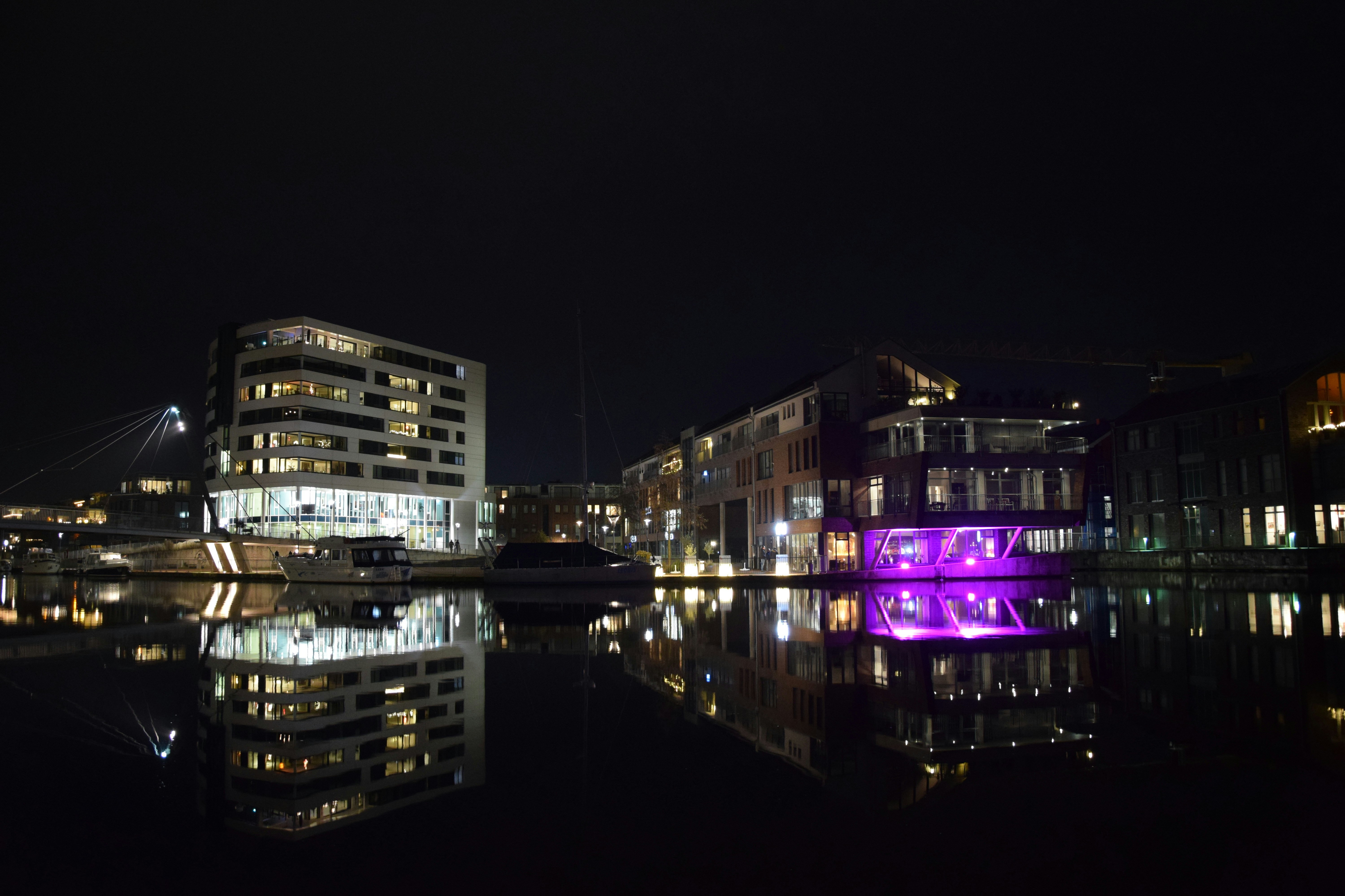 Modern buildings with vibrant lights reflecting on a calm waterfront at night.