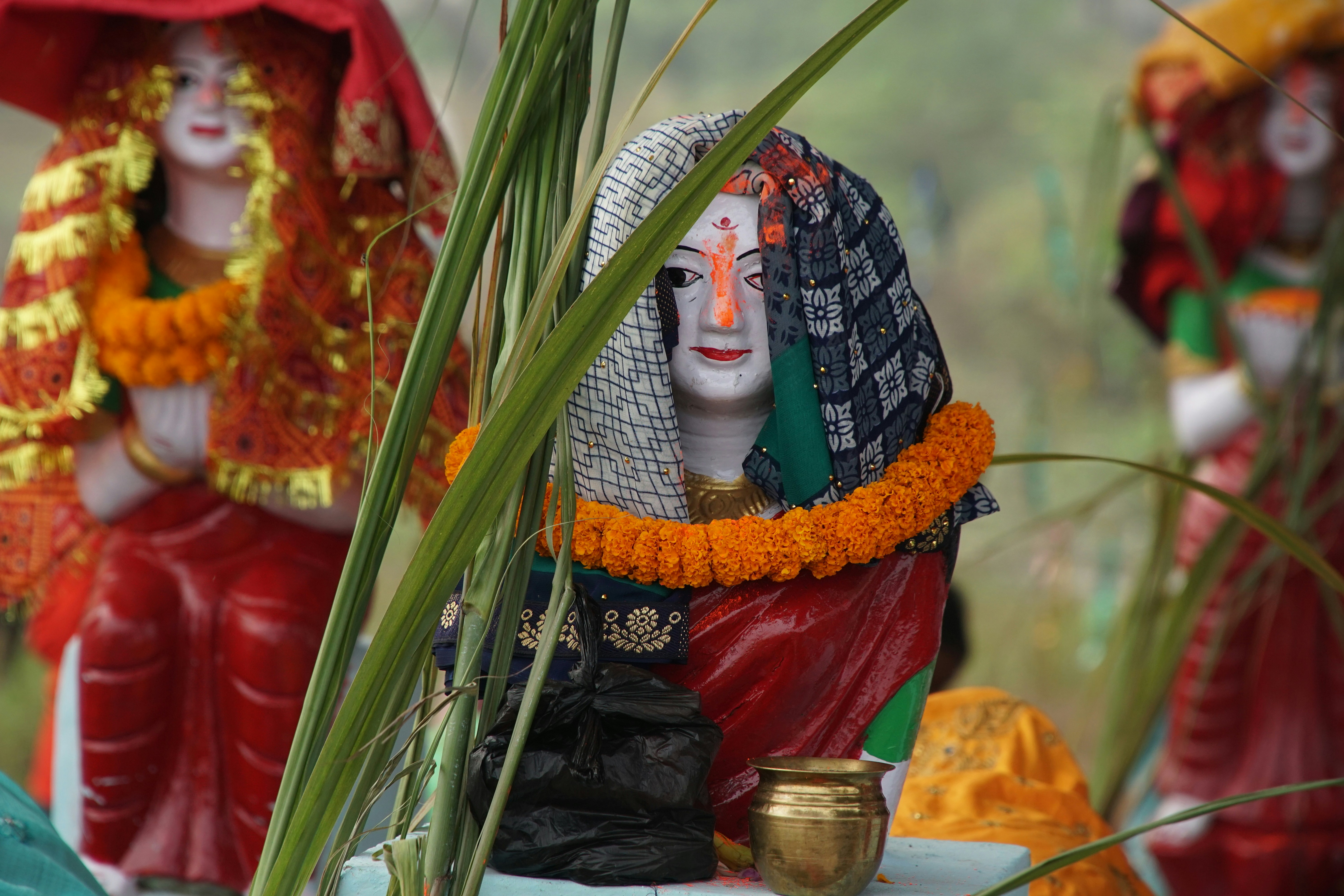 Colorful statues adorned with marigold garlands and traditional attire in a lush green setting.