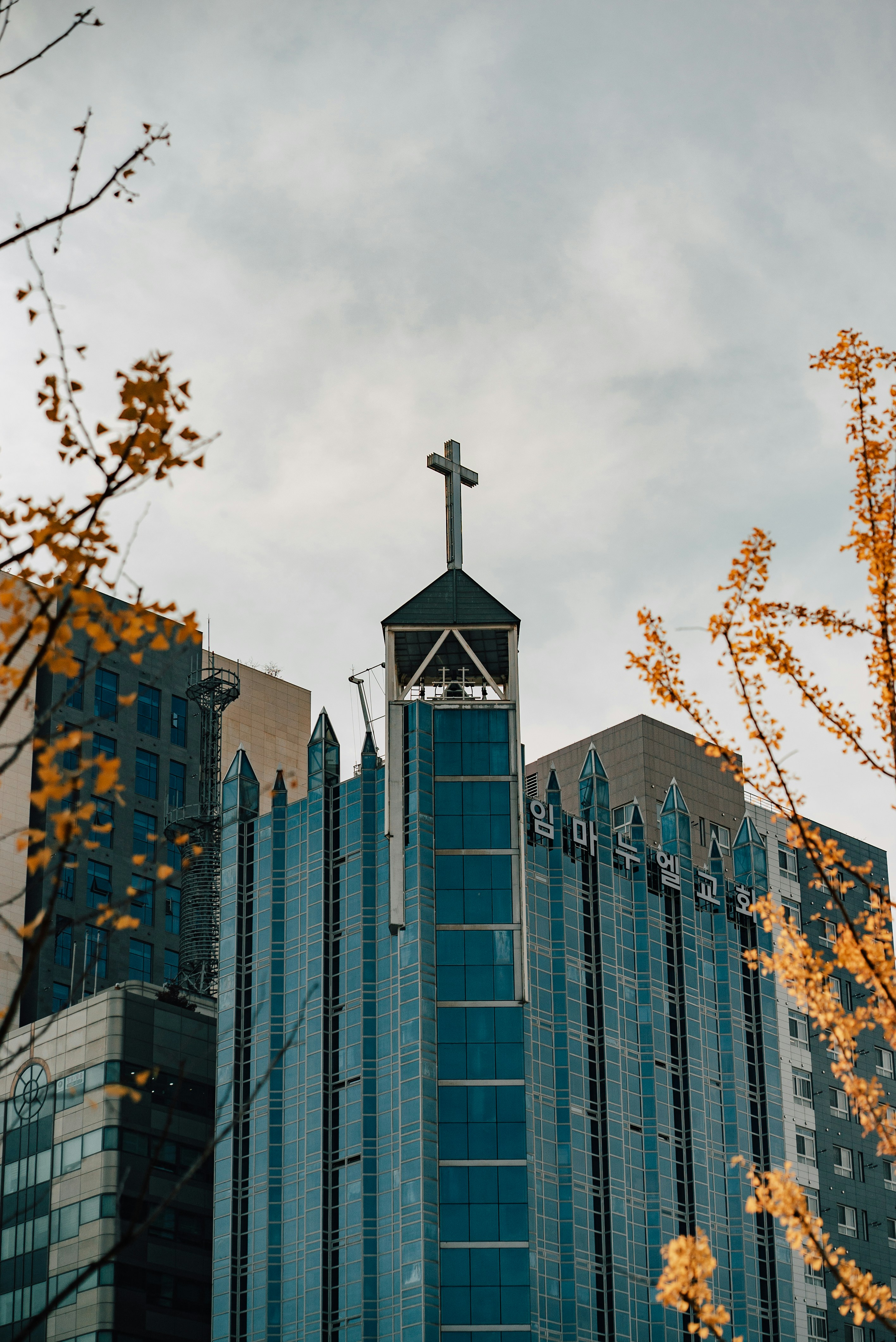 Cross-Topped Glass Tower Pierces an Autumn-Framed Cityscape