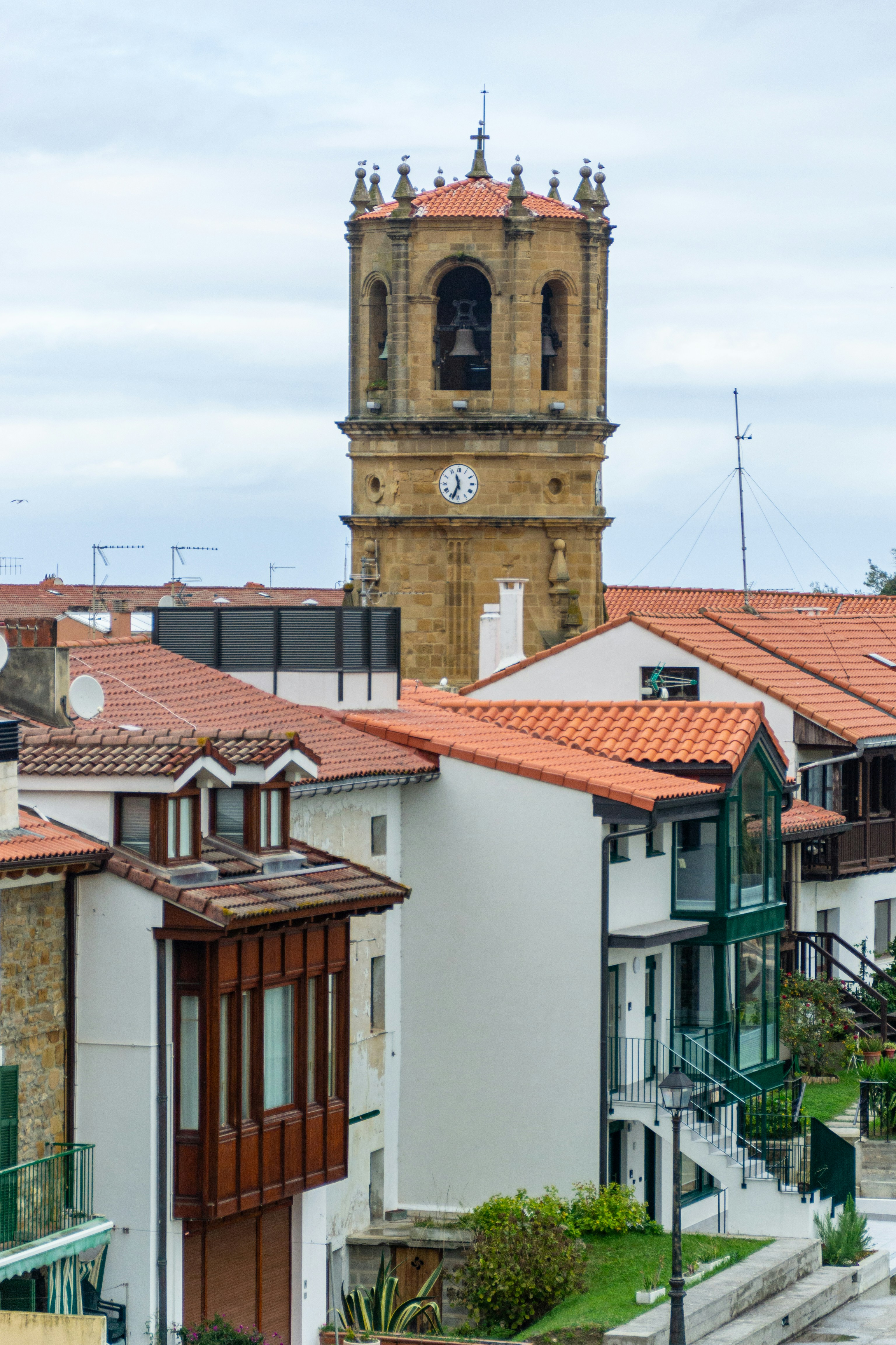 Historical clock tower rising above contemporary buildings in a coastal town, showcasing a blend of architectural styles.