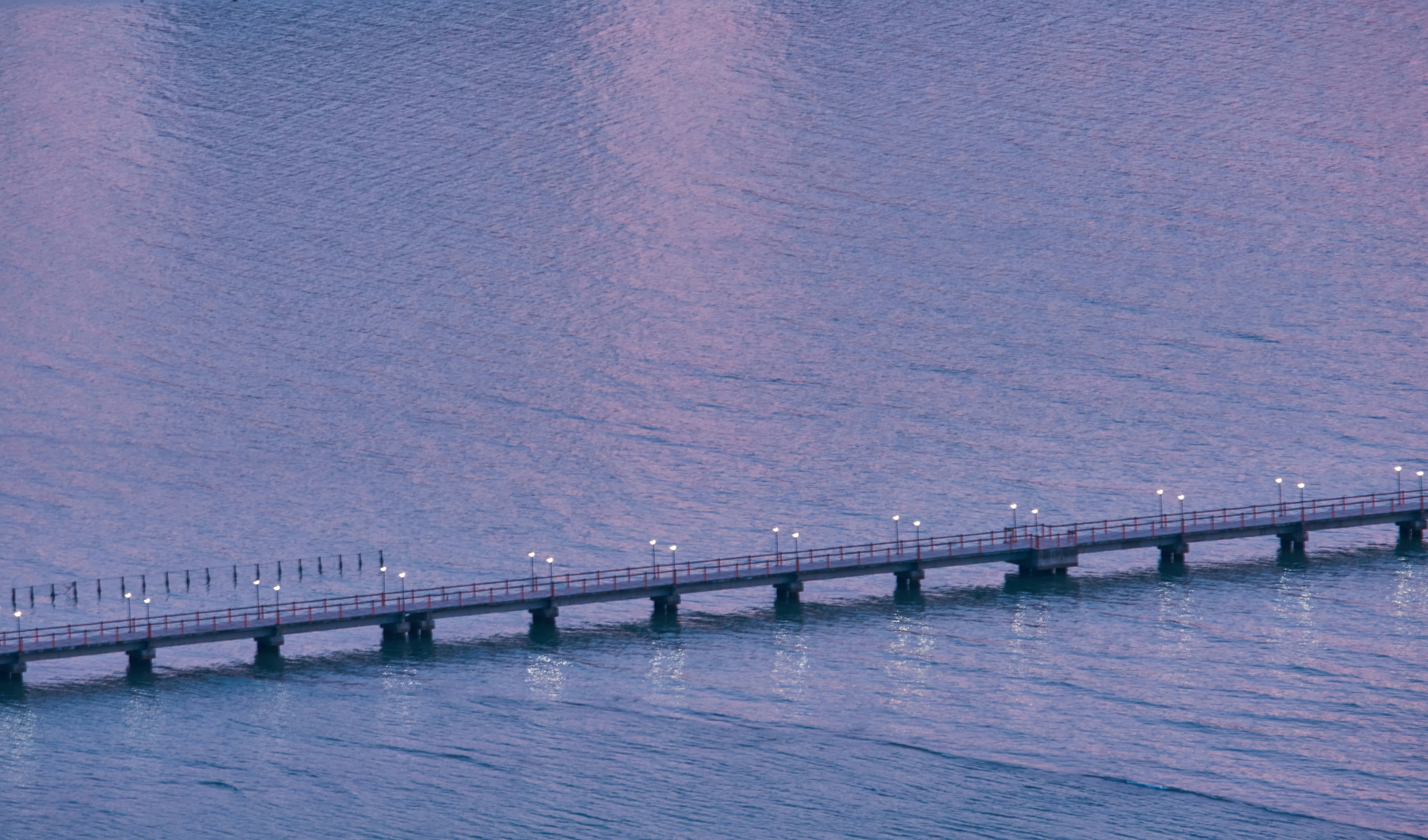 A serene pier extending into calm waters, illuminated by soft lights against a twilight backdrop.