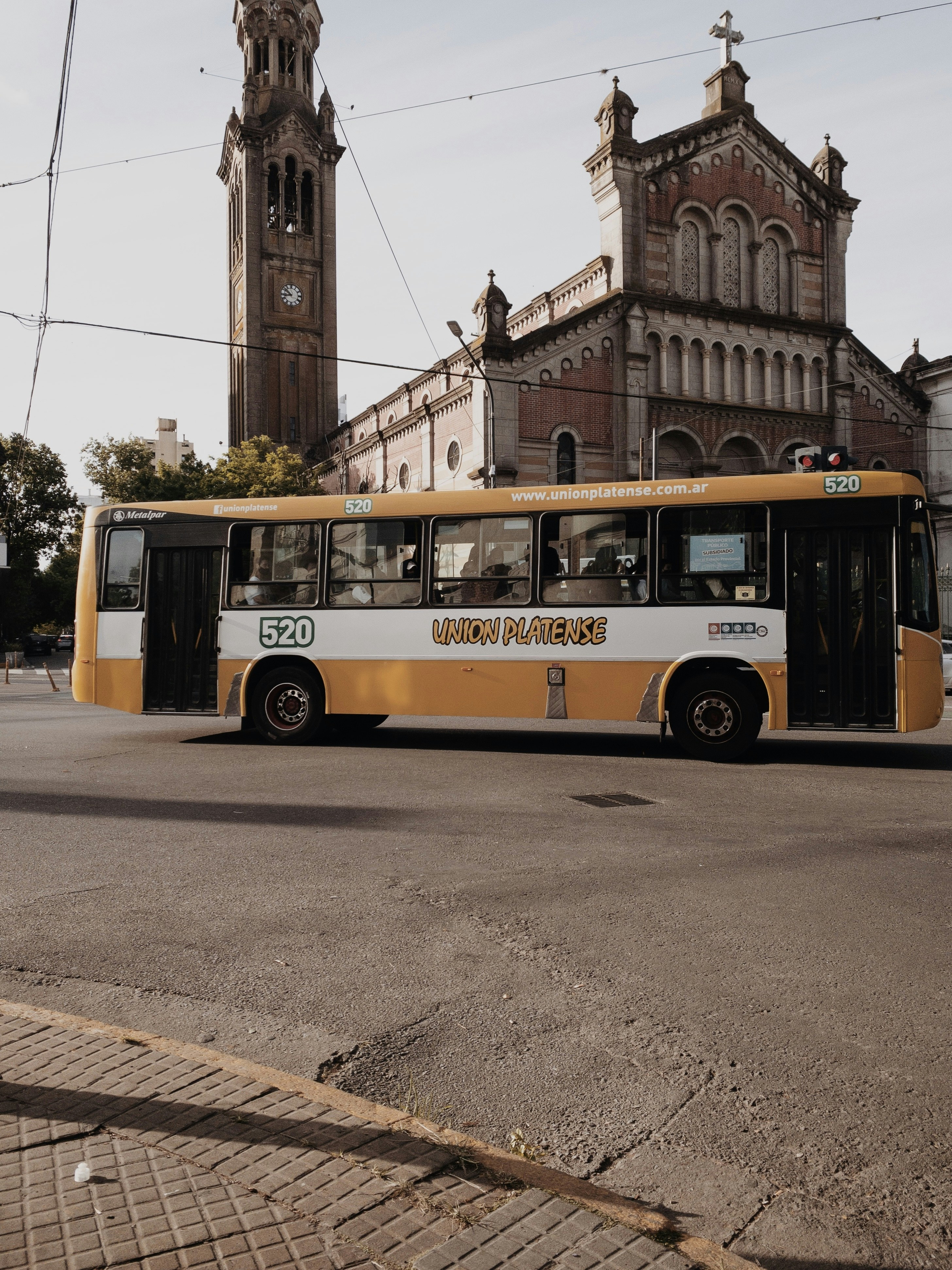 Golden City Transport: A Retro-Style Bus Pauses Before a Historic Brick Cathedral