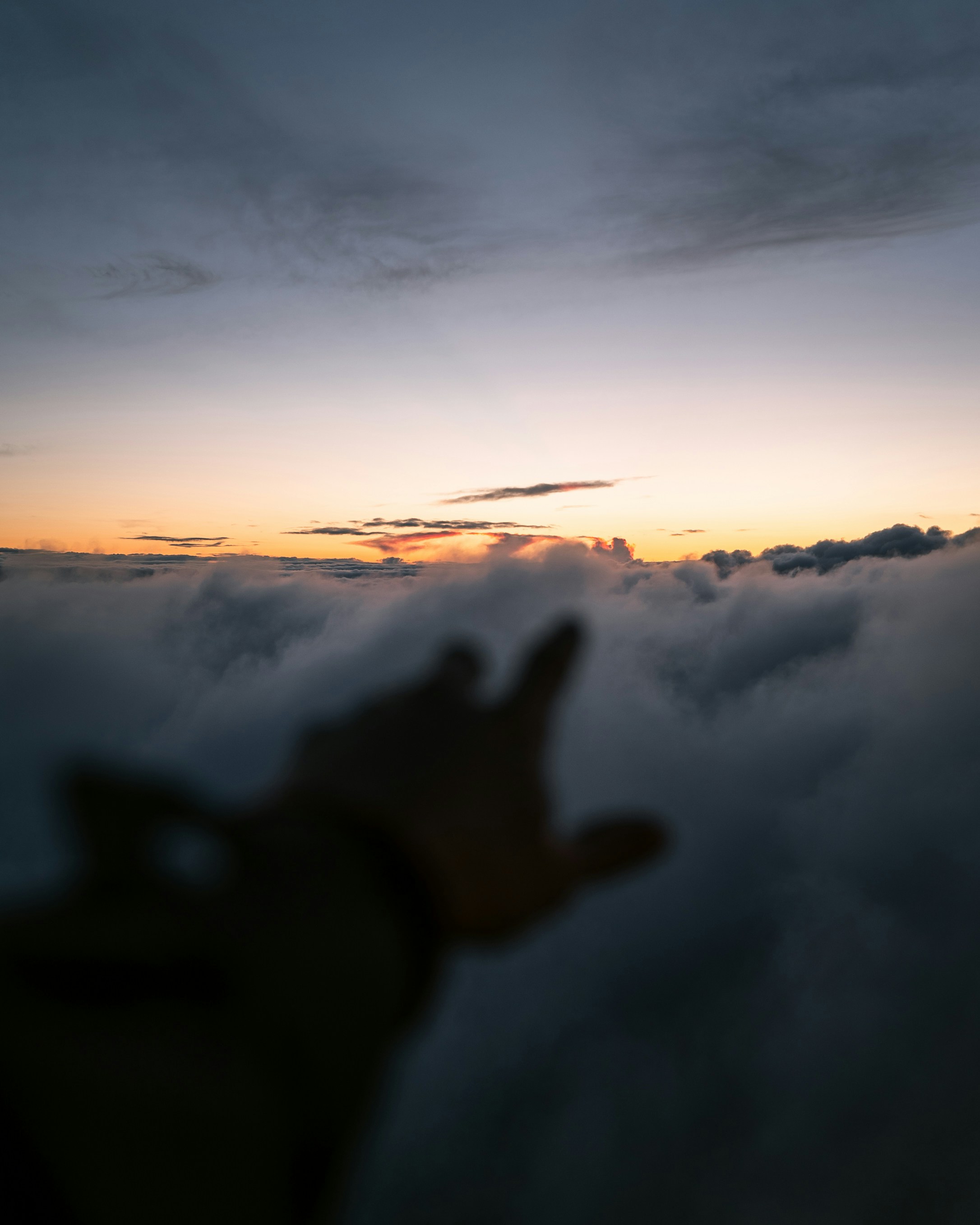 a person's hand reaching for the sky above the clouds