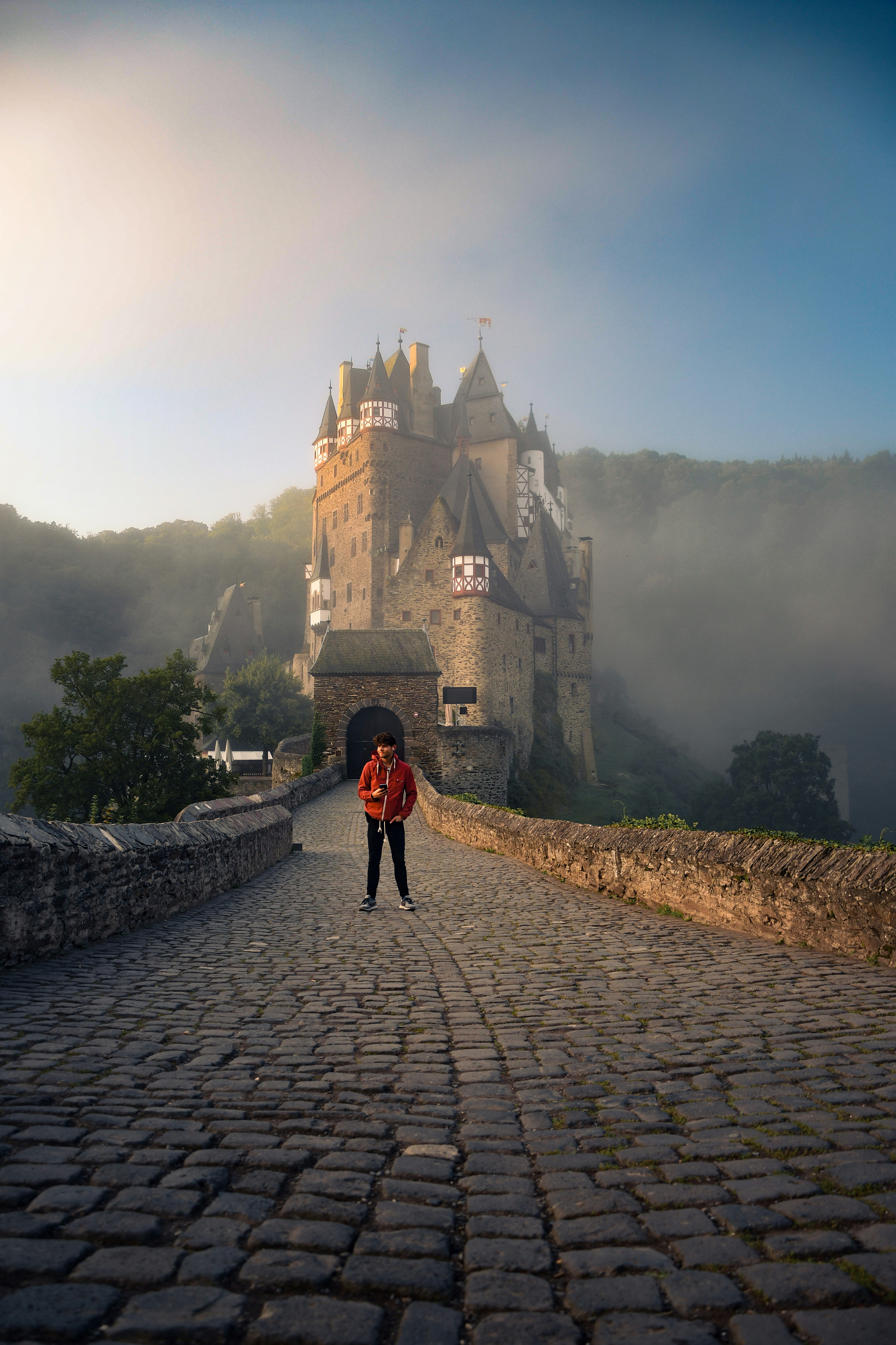 Red-clad Wanderer on a Cobblestone Path Toward a Misty Castle