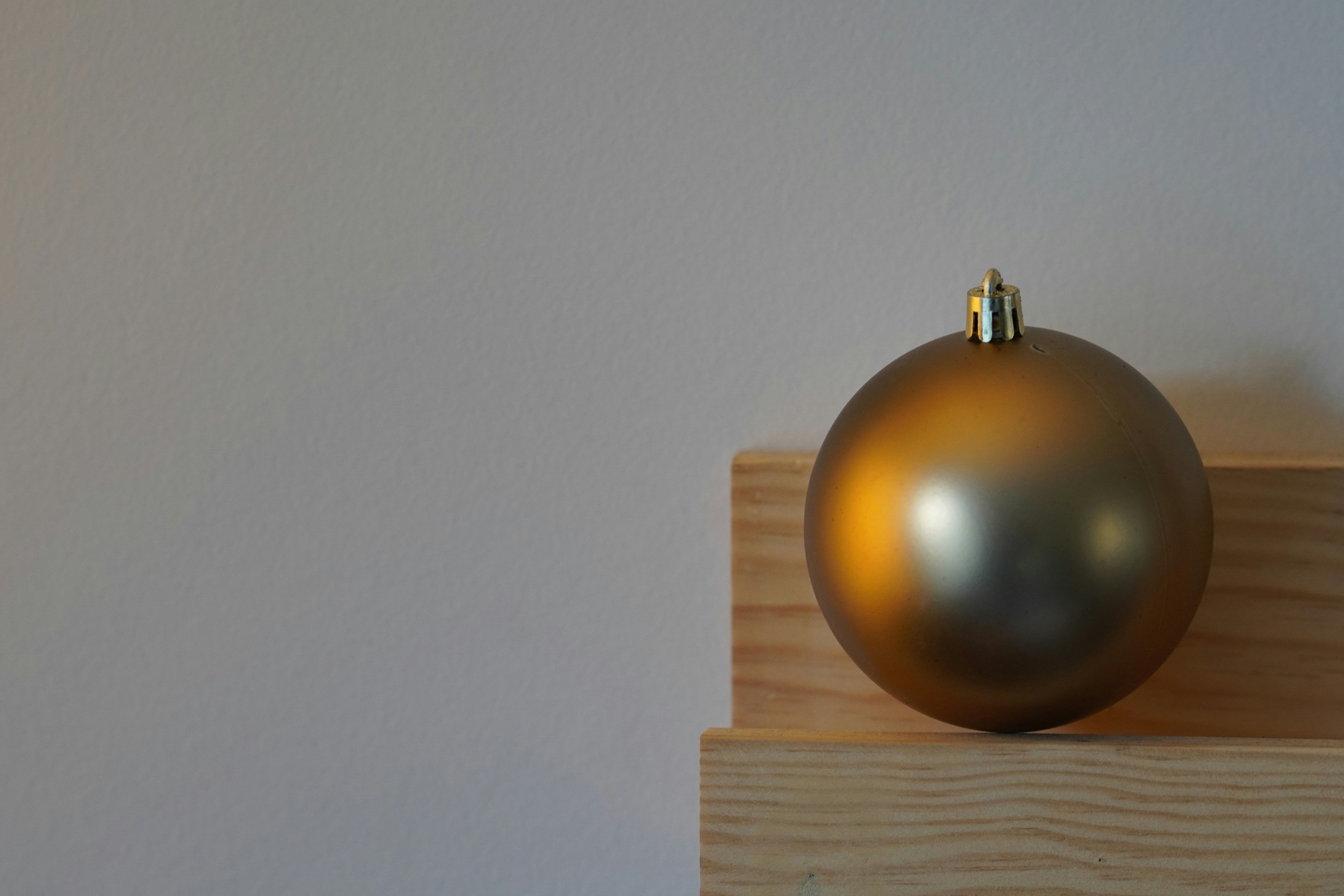 A golden ornament resting on a wooden ledge, highlighting its smooth surface against a neutral backdrop.