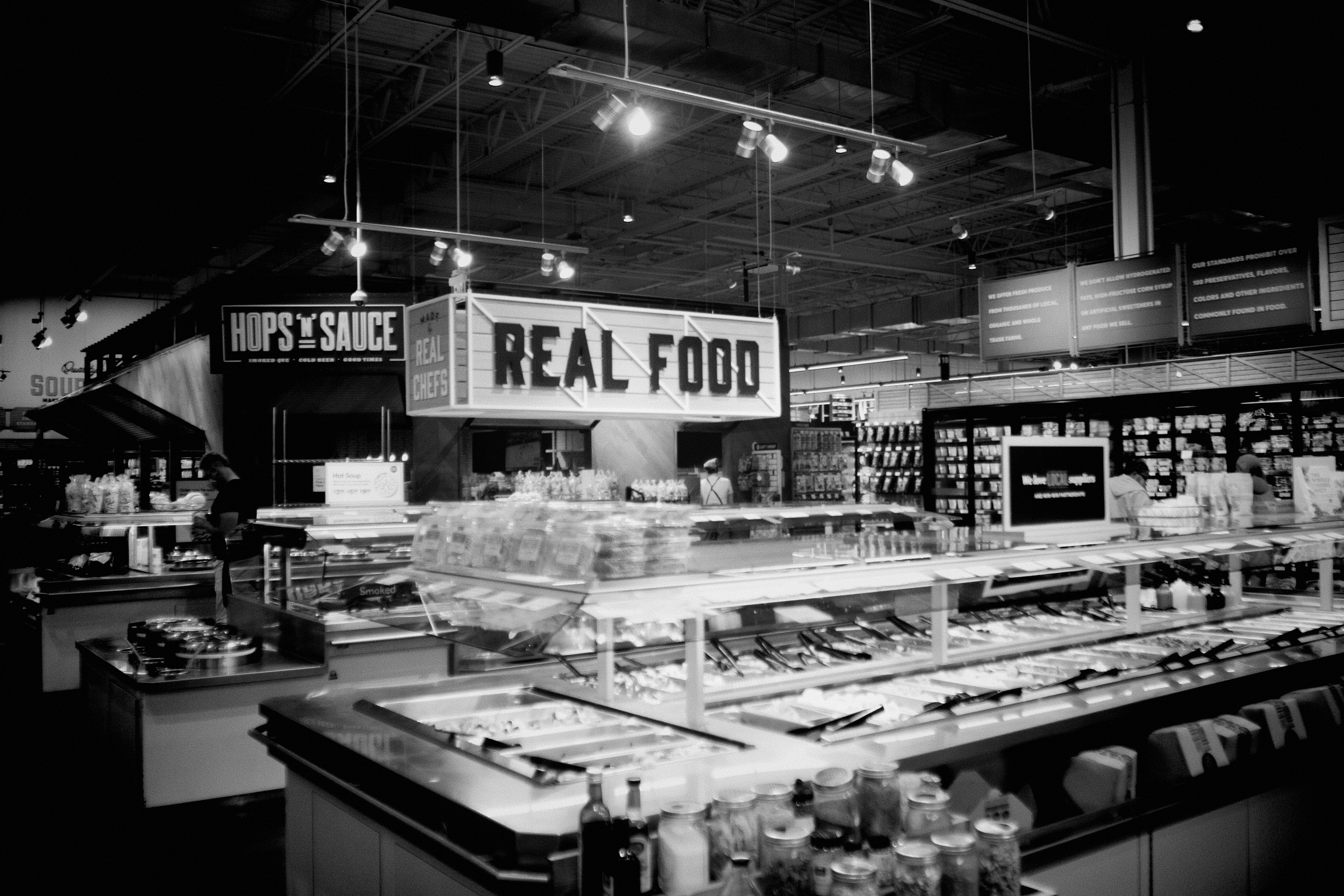 A bustling food display area in a market, showcasing a variety of fresh options under the sign 'REAL FOOD.' The ambiance suggests a focus on healthy eating.