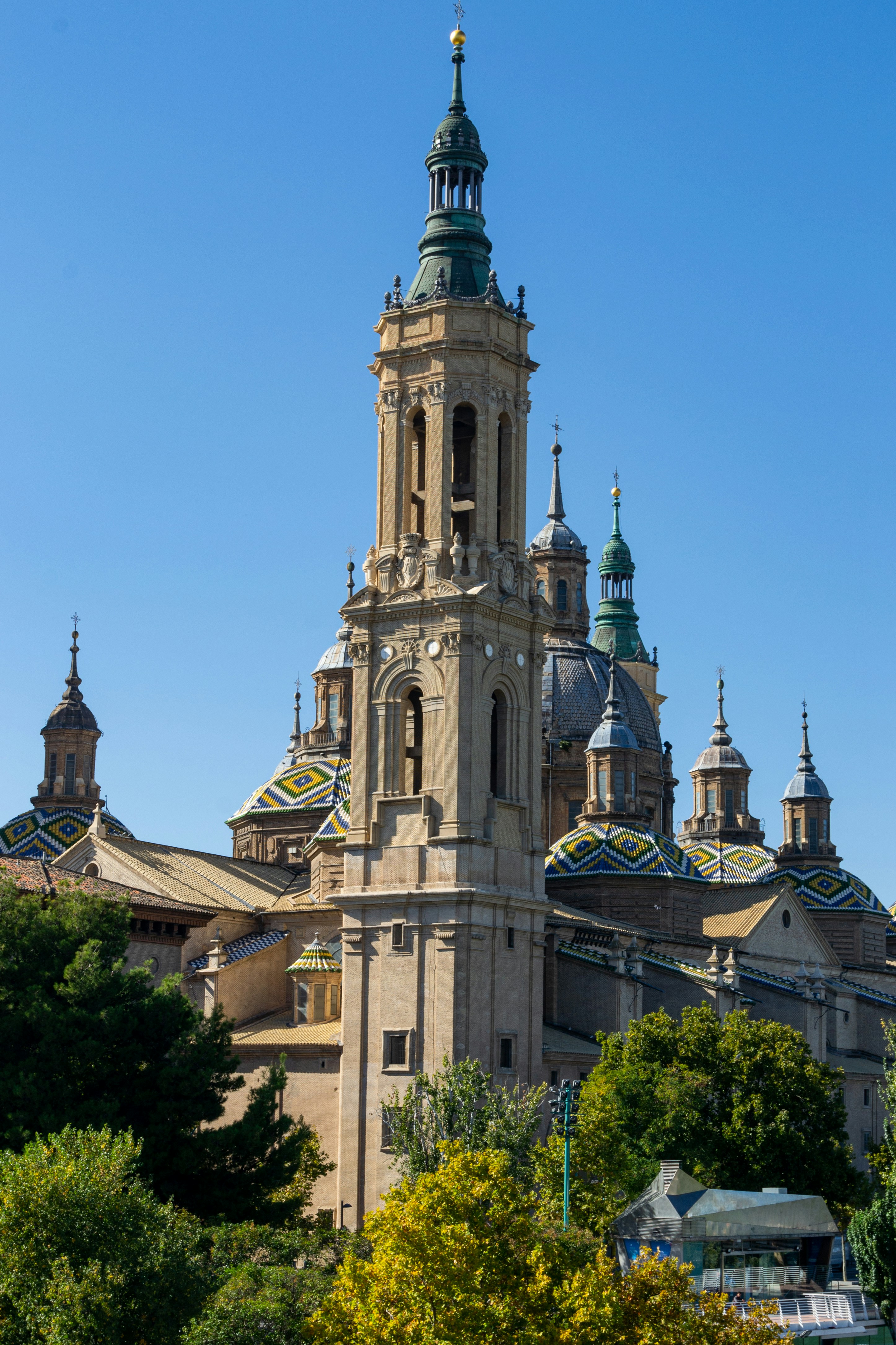 Majestic bell tower adorned with intricate details, surrounded by vibrant foliage against a clear blue sky.