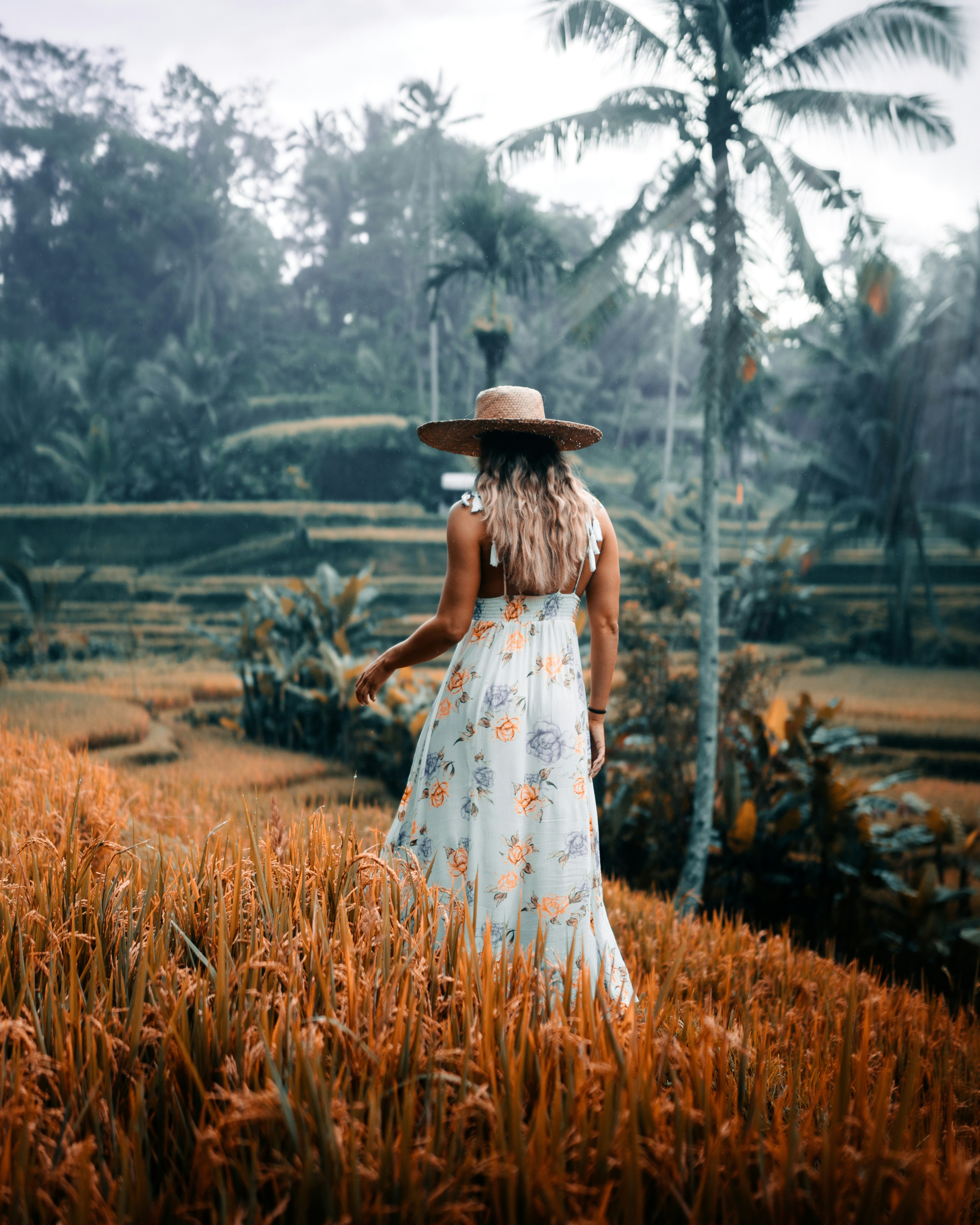 A woman in a floral dress strolls through vibrant rice terraces under a soft, misty sky, embodying tranquility and connection to nature.