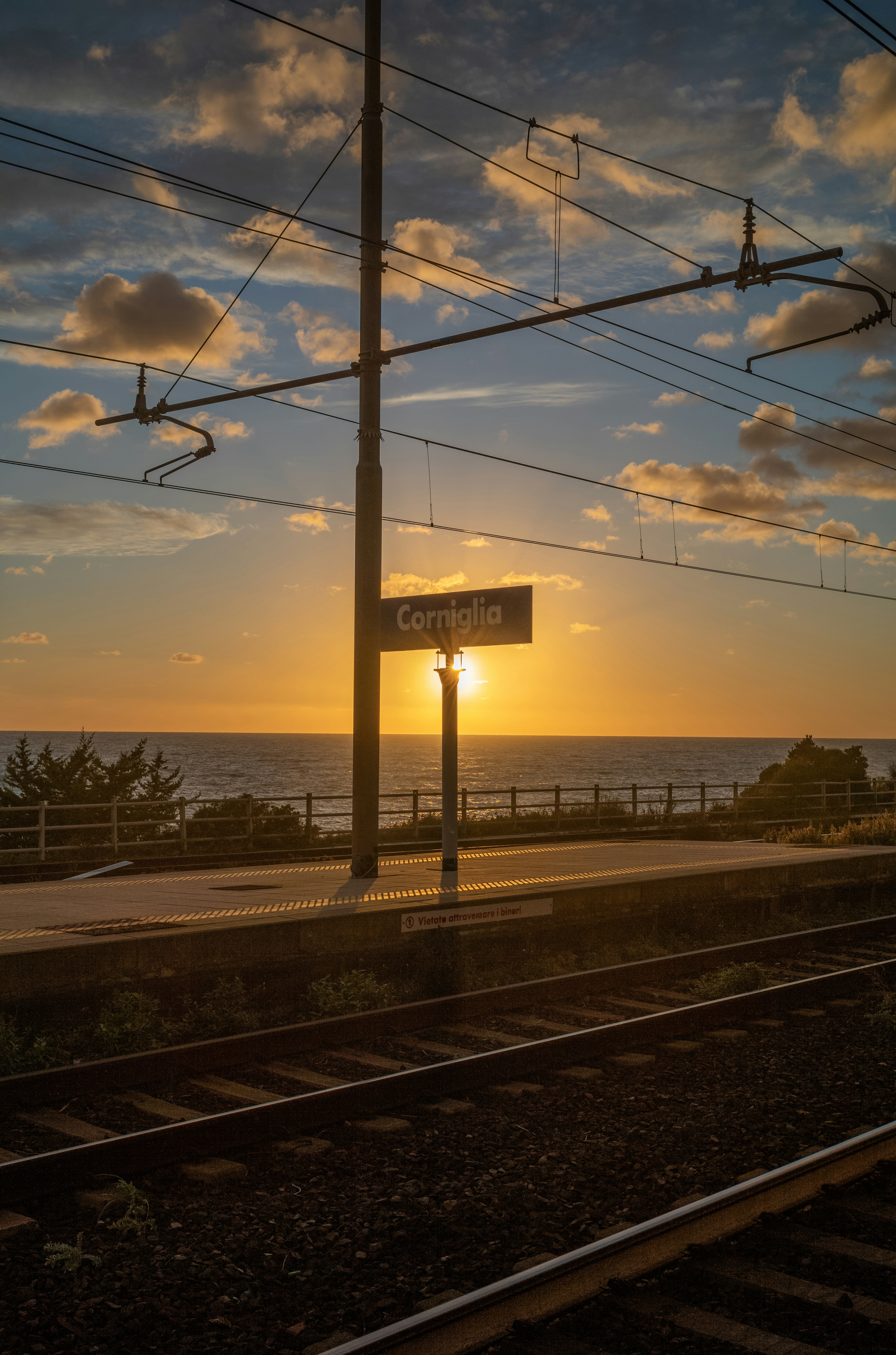 Corniglia train station sign silhouetted against a vibrant sunset over the ocean, capturing the tranquil moment of day’s end.