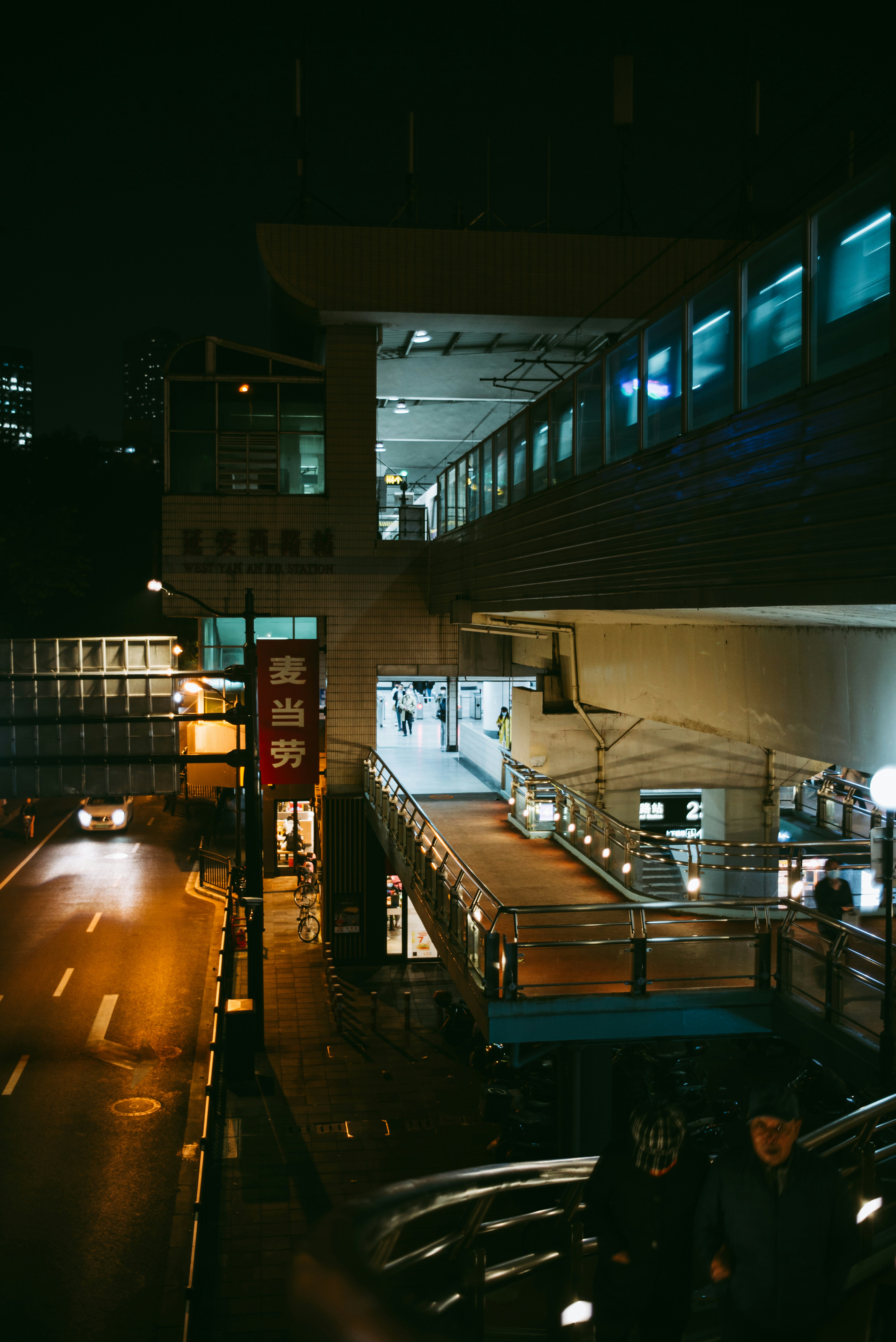 Busy urban scene at night, featuring a train station with illuminated pathways and pedestrians navigating the bustling environment.