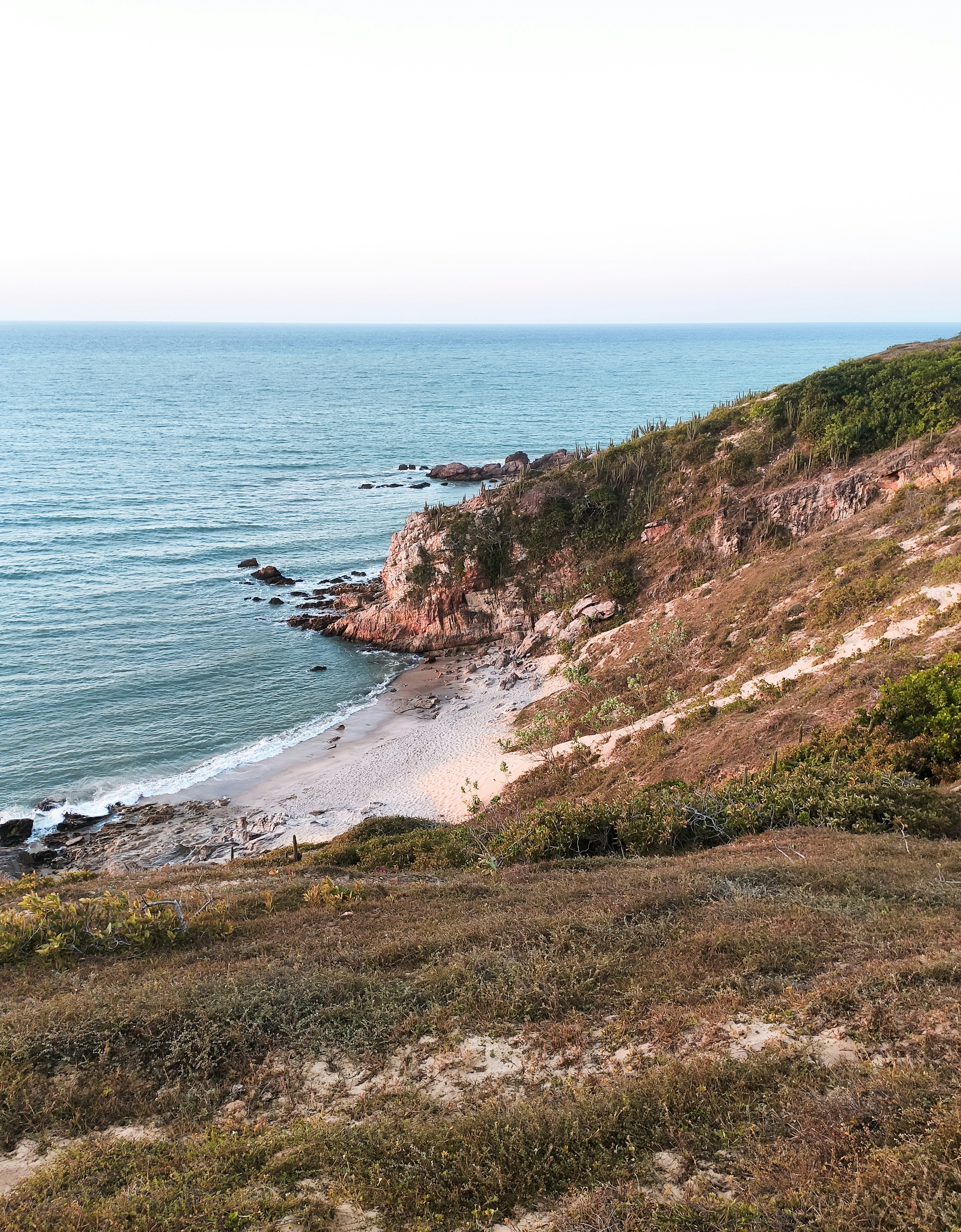 Gentle waves lapping against a secluded beach, framed by rugged cliffs and lush greenery. The tranquil scene evokes a sense of peace and natural beauty.