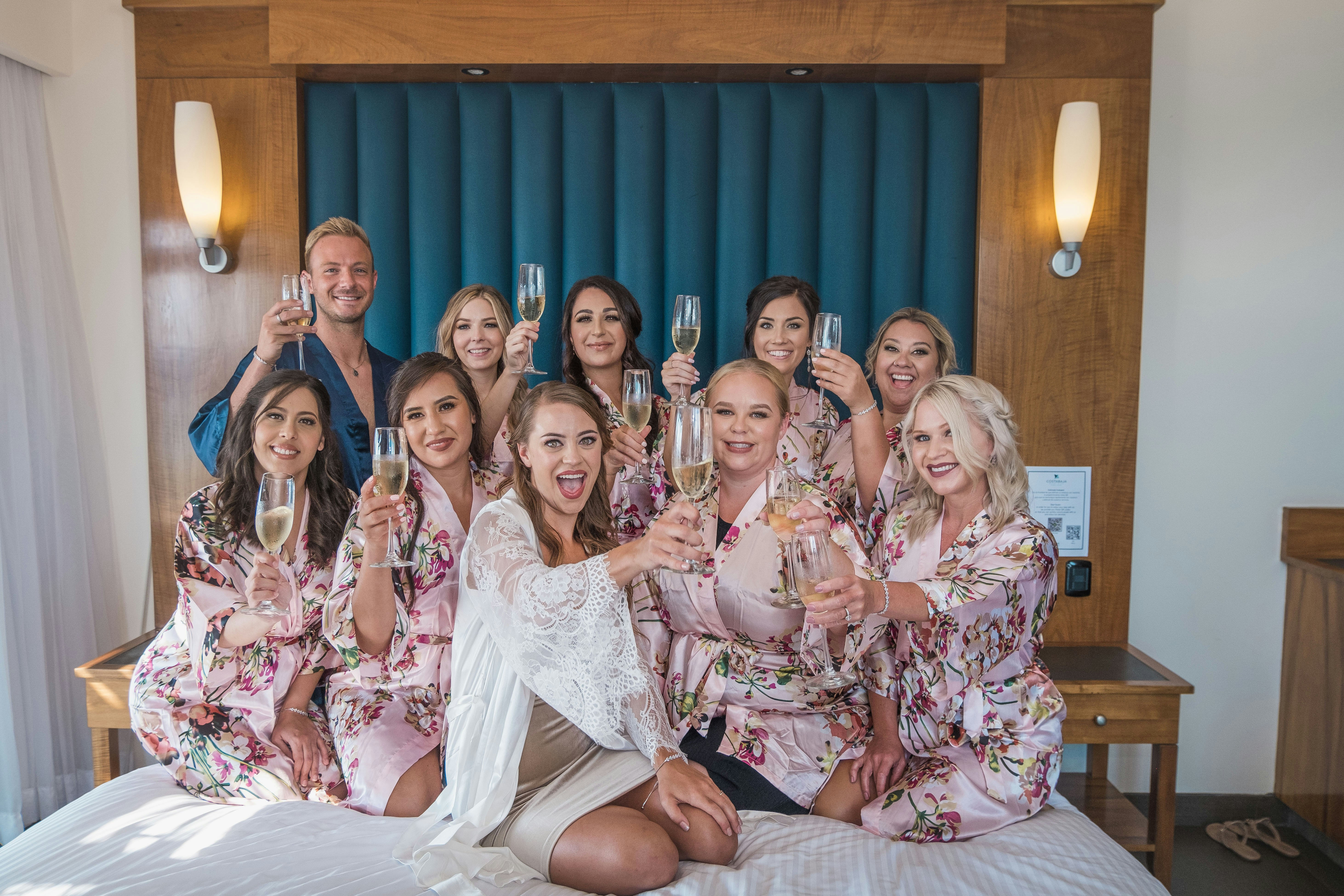 Group celebrating with champagne in floral robes on a bed.