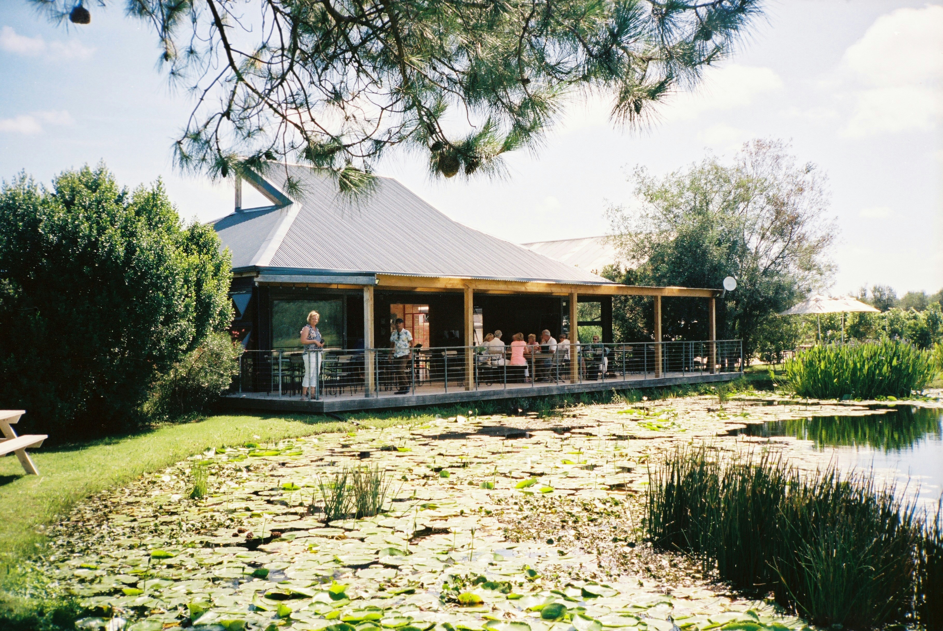 A group of people sitting on a porch next to a pond photo – Free Land ...