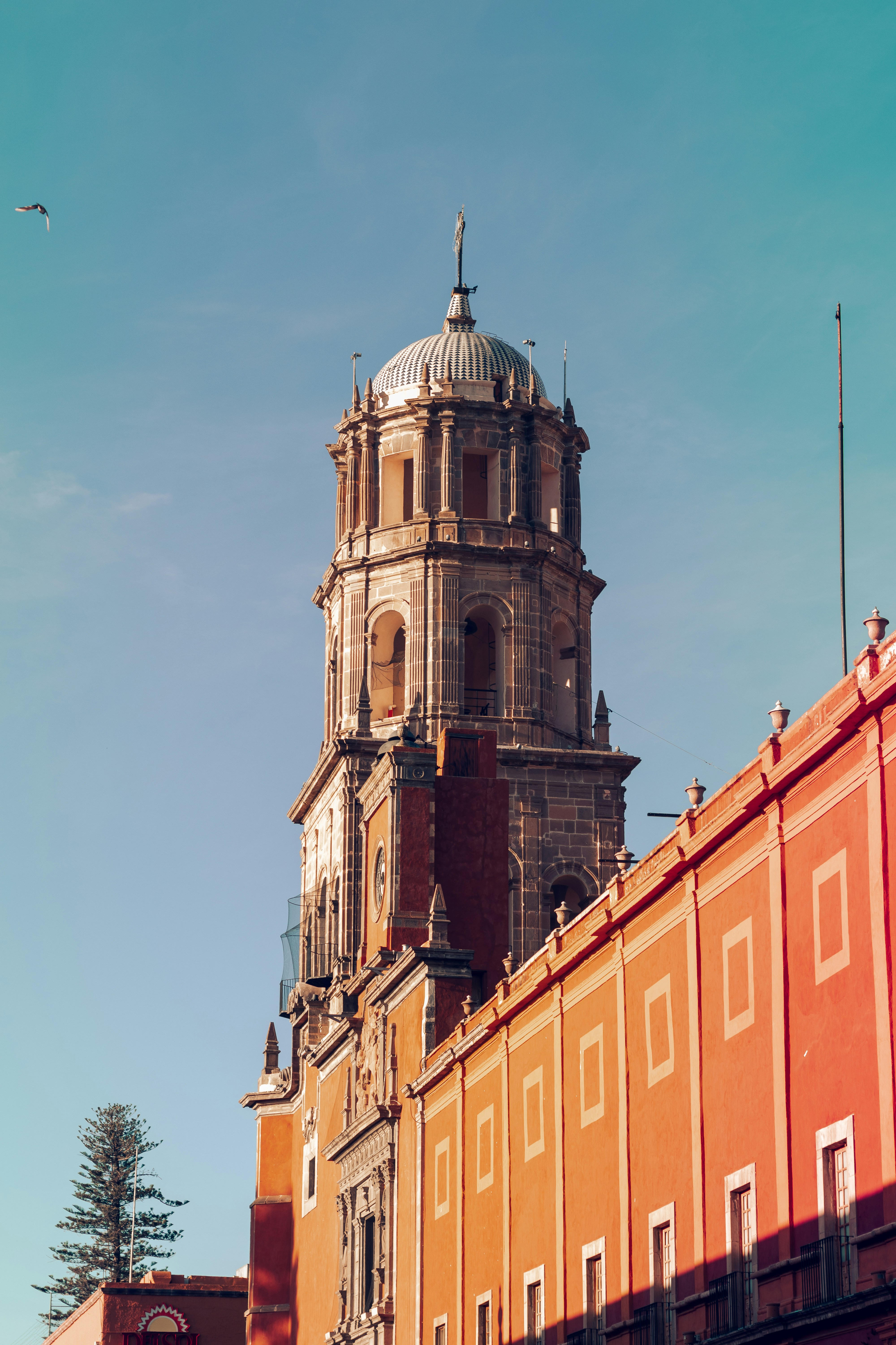 Historic bell tower rising above vibrant architecture under a clear sky. The structure showcases intricate details and a striking dome.