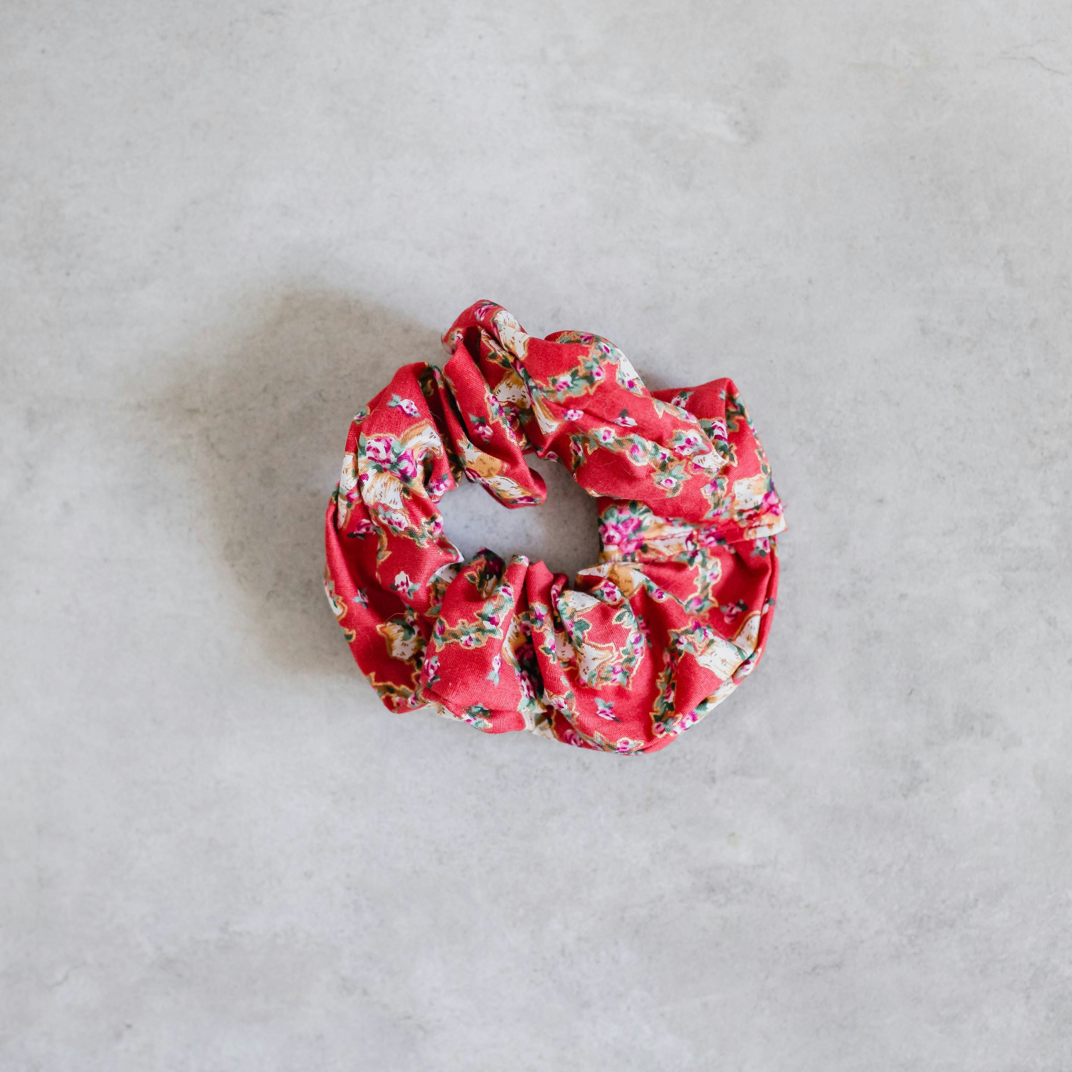 Vibrant red scrunchie adorned with delicate floral patterns, resting on a neutral surface.