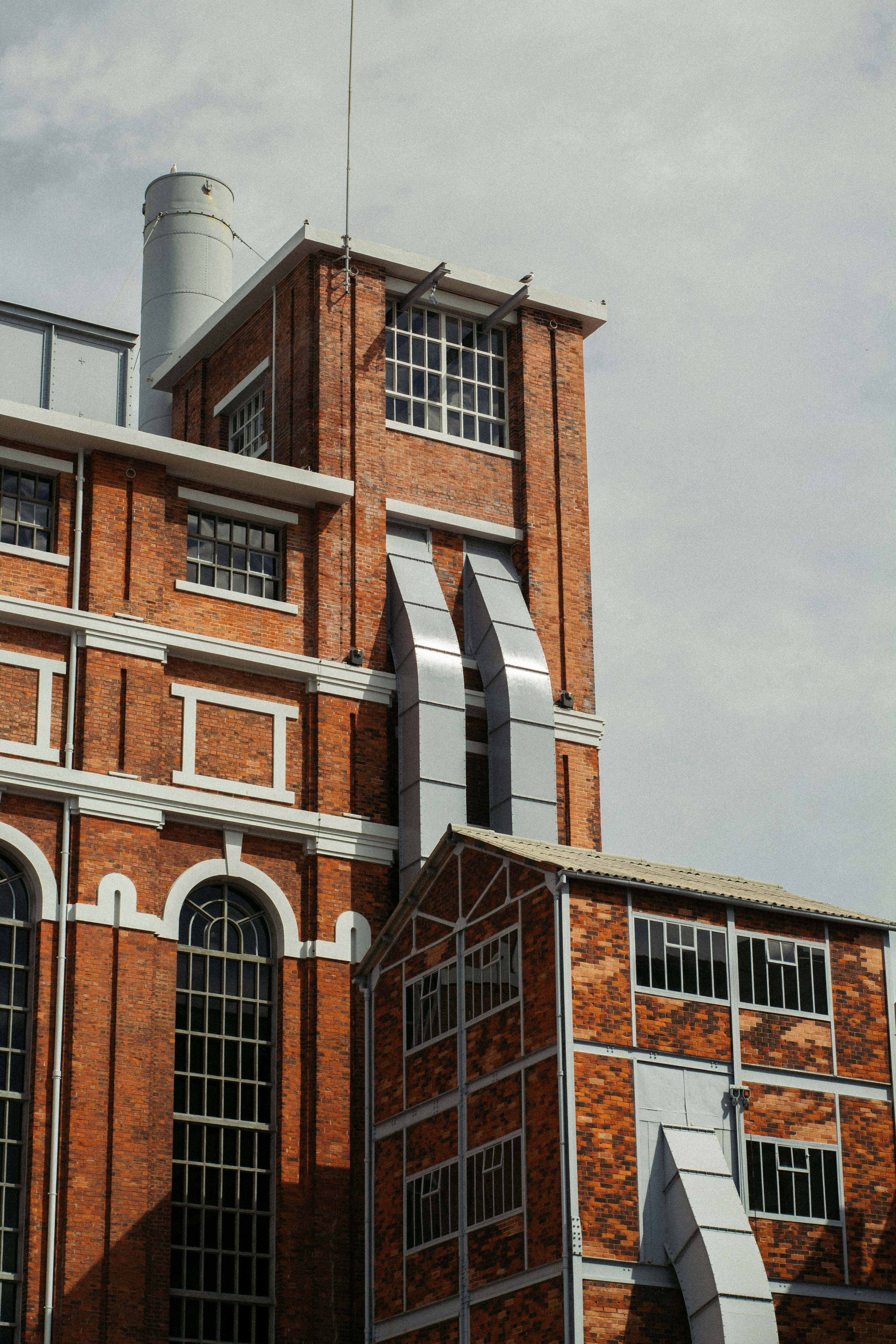 Red brick industrial building with large windows and metallic ducts, showcasing a blend of historical architecture and modern design elements.