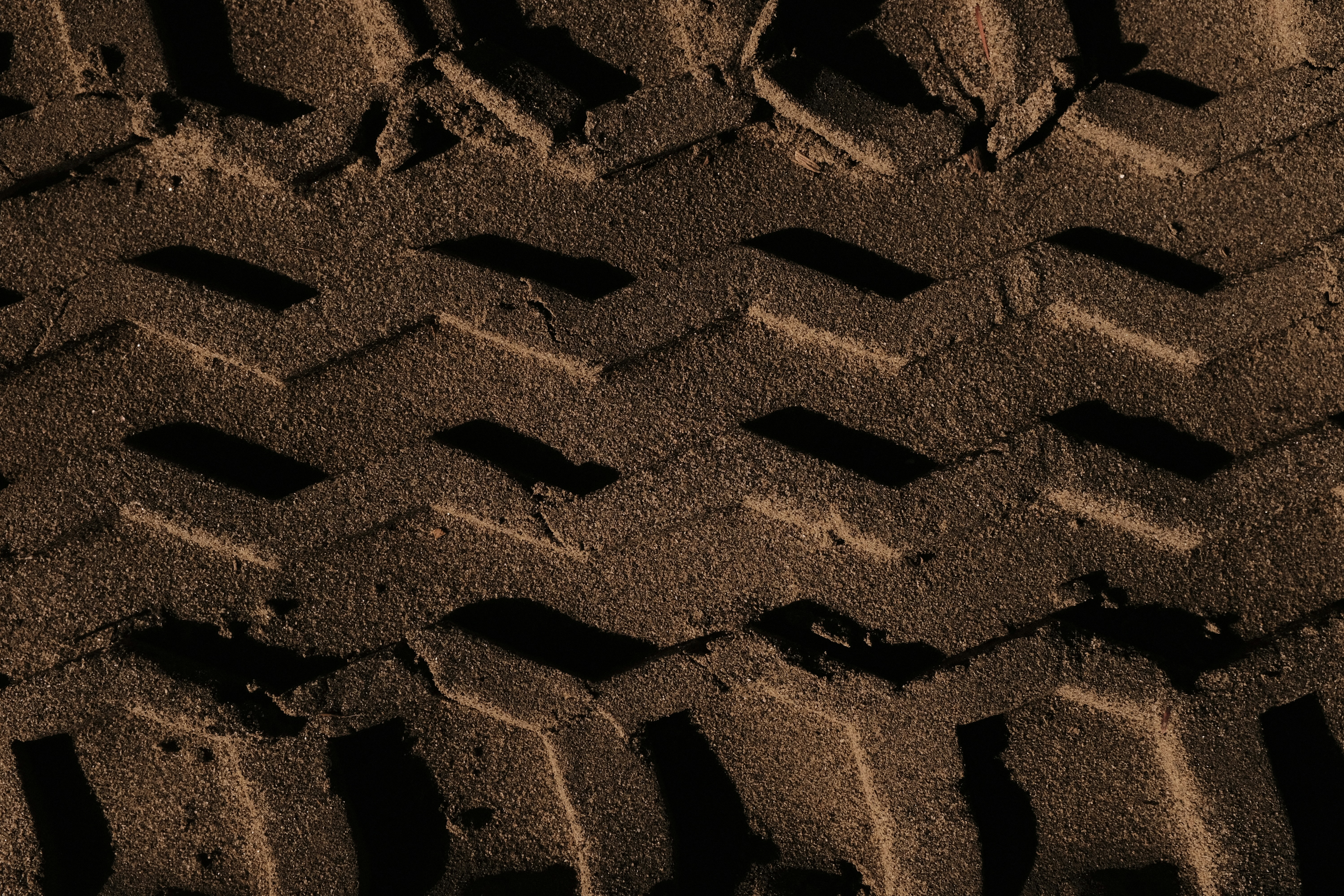 Close-up of tire tread imprints on sandy ground, showcasing intricate patterns and textures. The marks tell a story of movement and exploration.