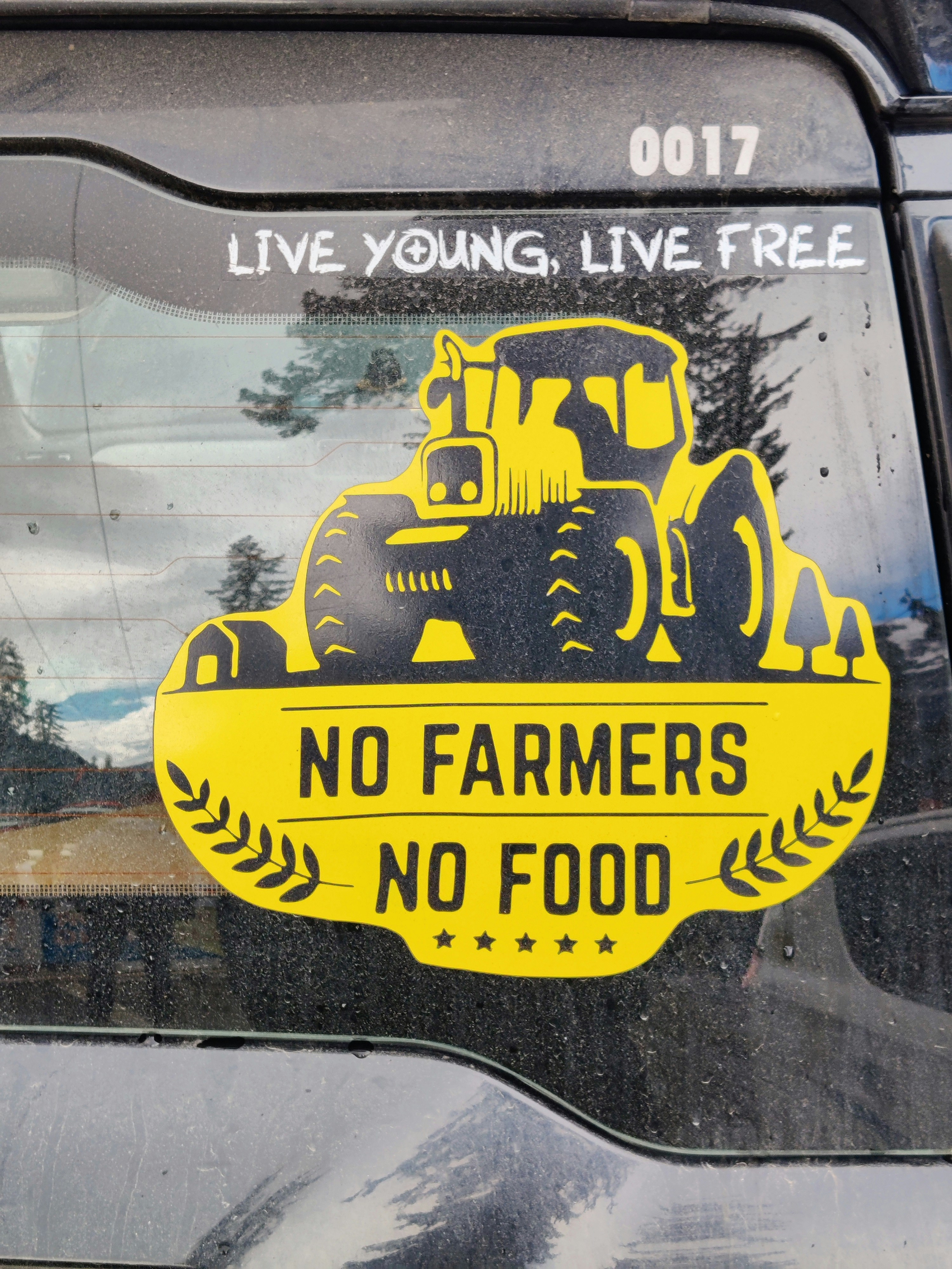 Bold yellow tractor decal with the phrase 'NO FARMERS NO FOOD' prominently displayed on a vehicle's rear window.