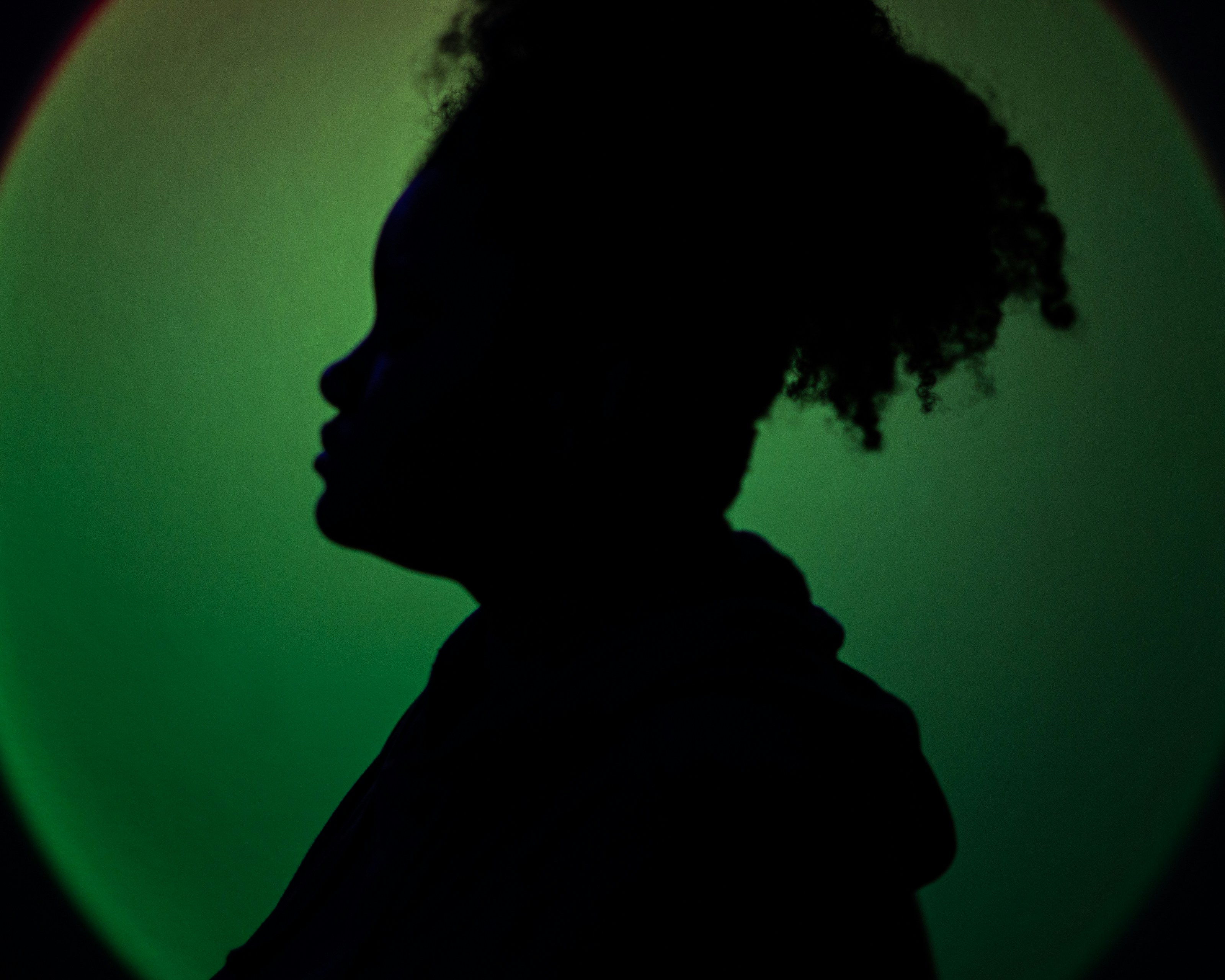 Silhouette of a child against a vibrant green and blue light gradient, highlighting the contours of their profile.