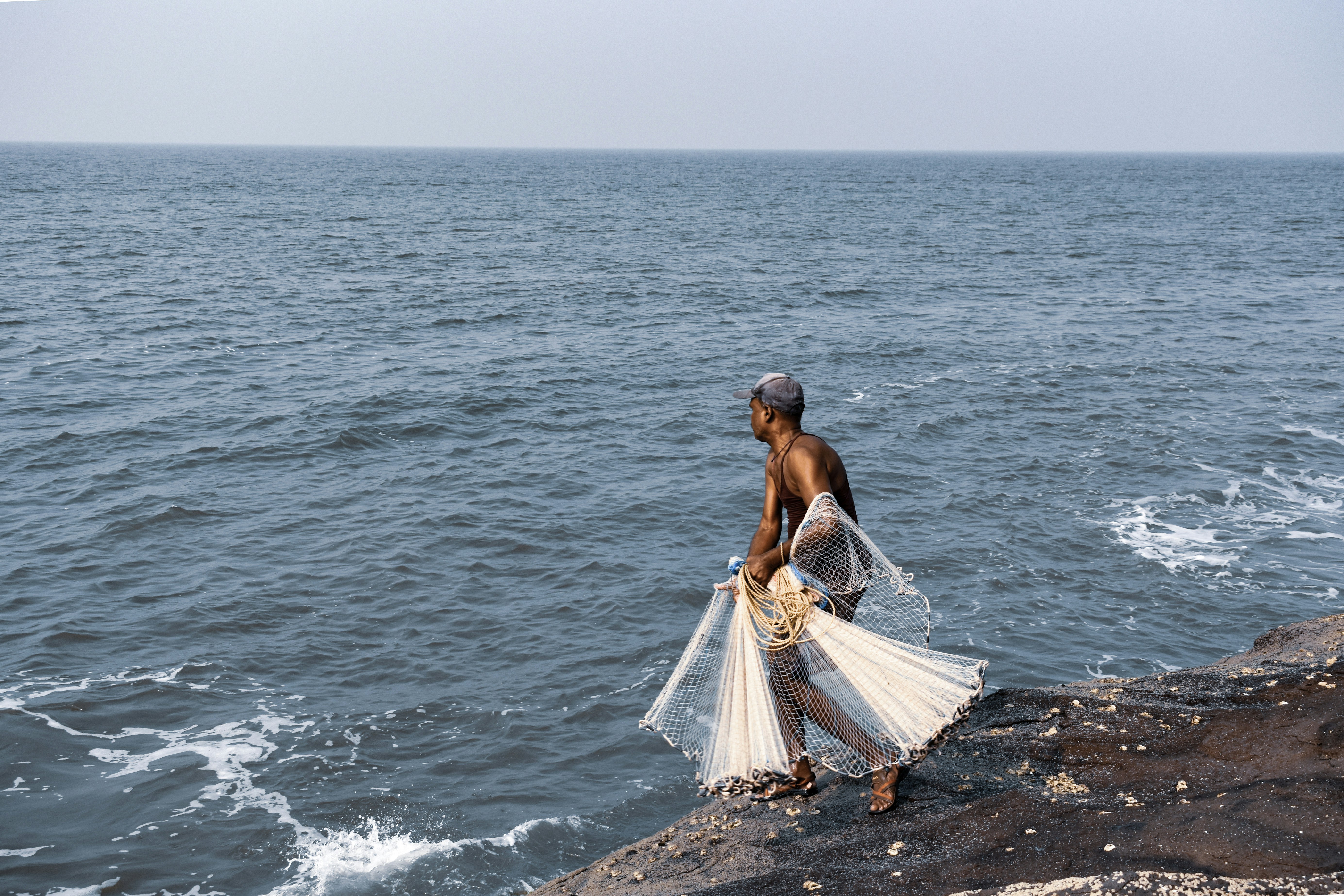 Seaward Stance: A Bare-Chested Fisherman Grasping White Nets on a Rocky Edge