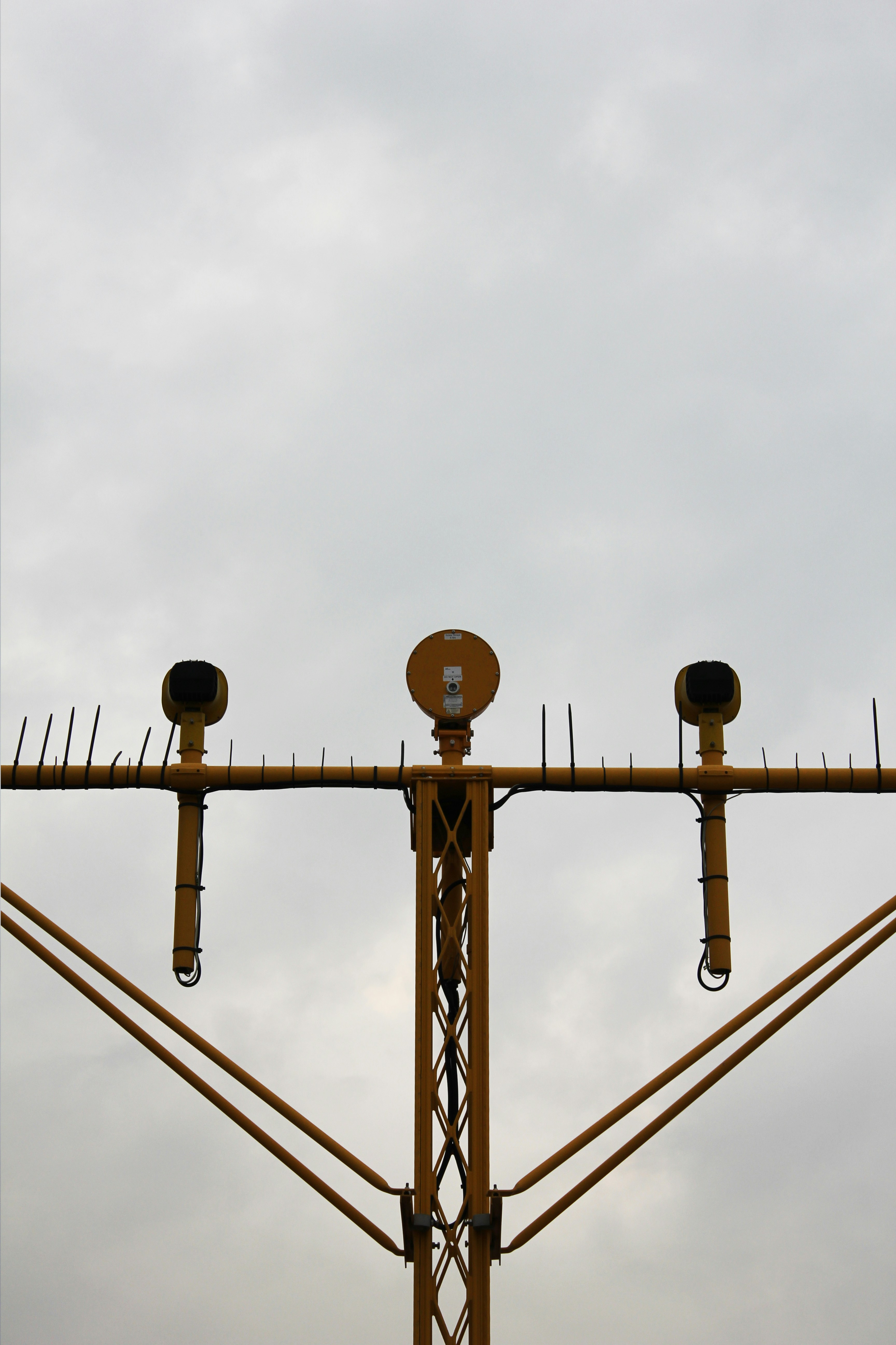 Yellow communication tower with antennas and sensors, standing against a cloudy sky.
