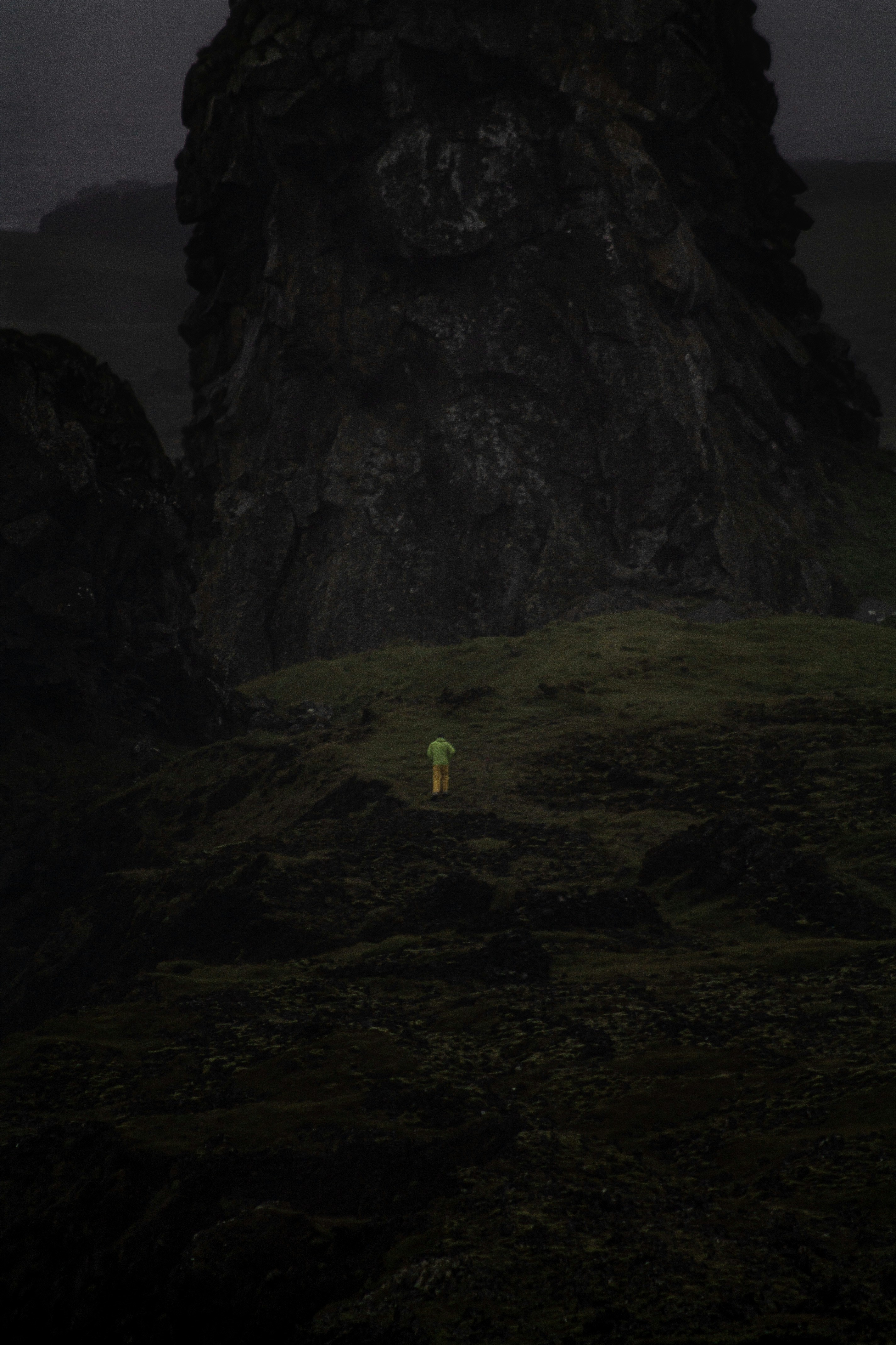 A lone figure in bright attire traverses a rugged landscape dominated by towering rock formations, evoking a sense of scale and solitude.